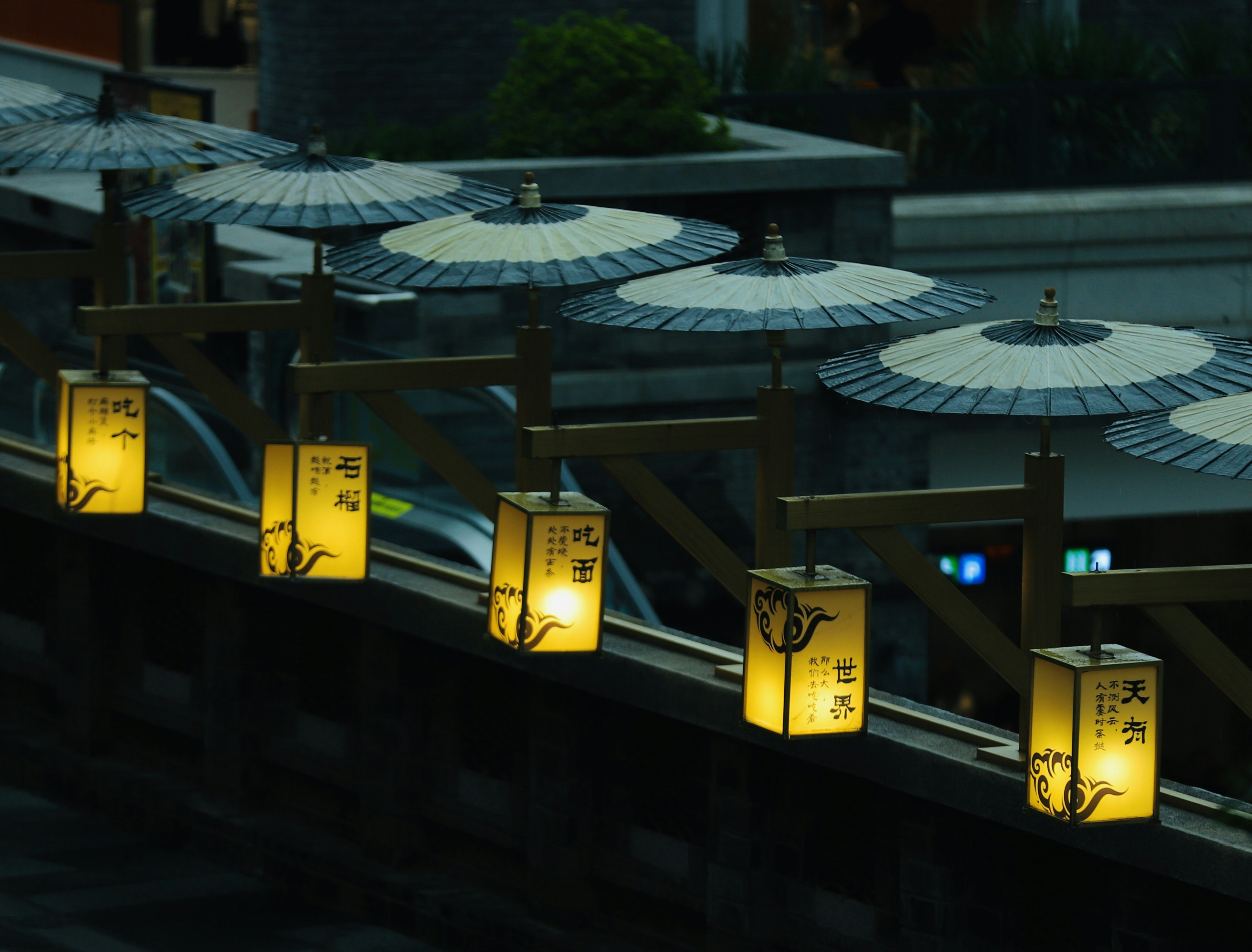 Lantern Chorus Along a Shadowed Walkway Beneath Indigo Umbrellas