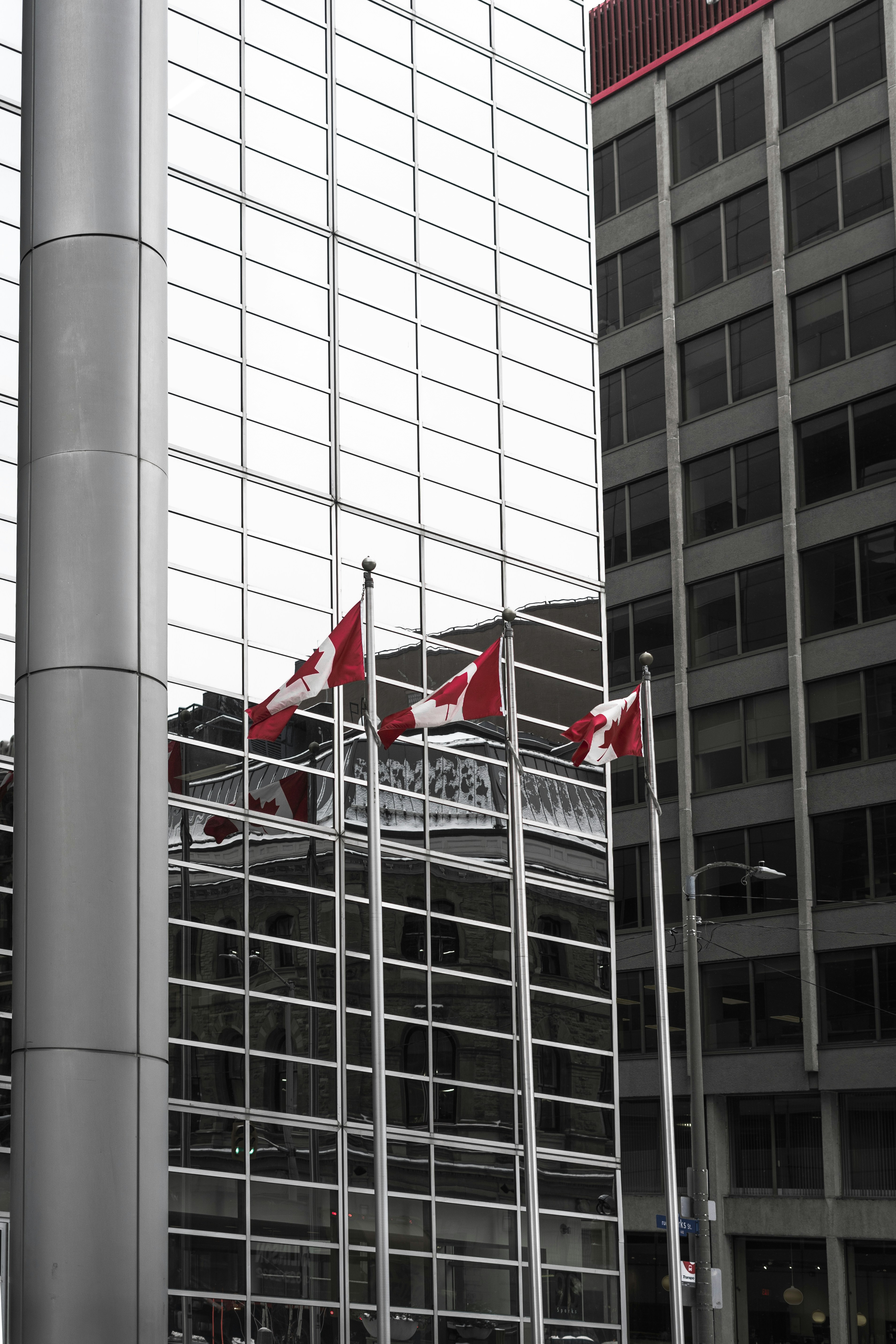 The canadian flag is flying in front of a glass building photo – Free ...