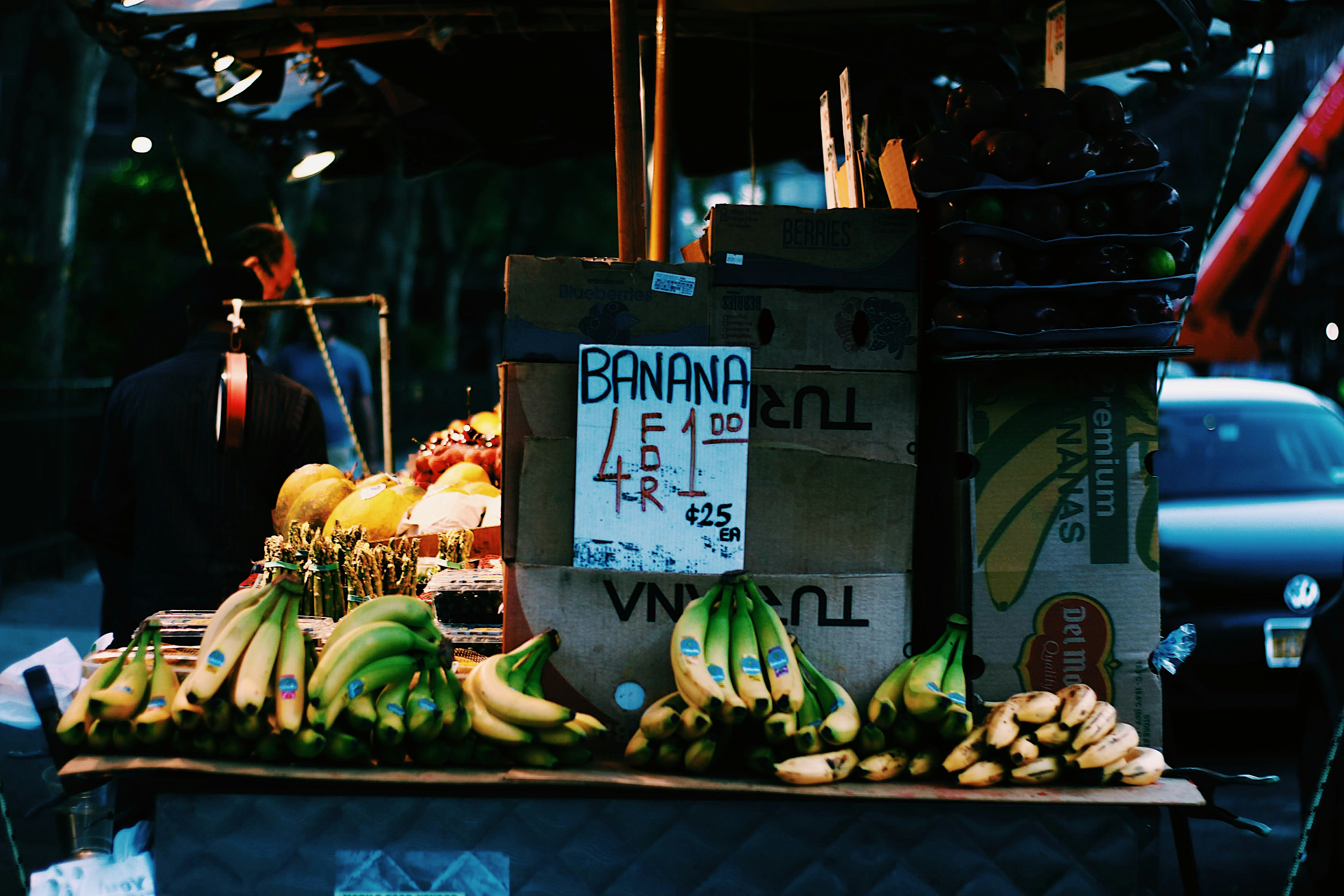 Bananas and other fruits displayed on a street vendor's cart illuminated by warm evening light.