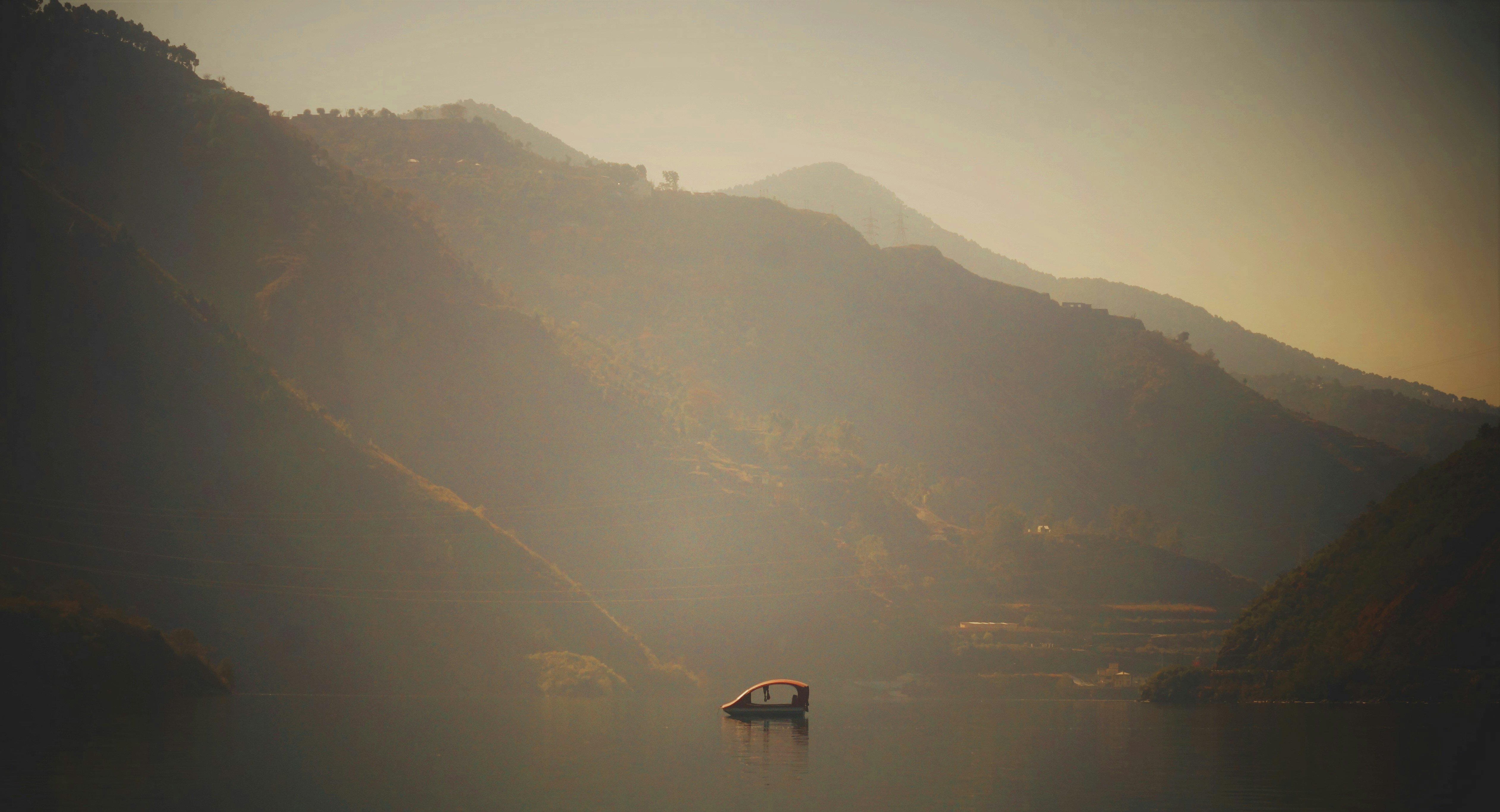 A lone boat drifts on a serene lake surrounded by misty mountains, evoking a sense of tranquility and isolation.