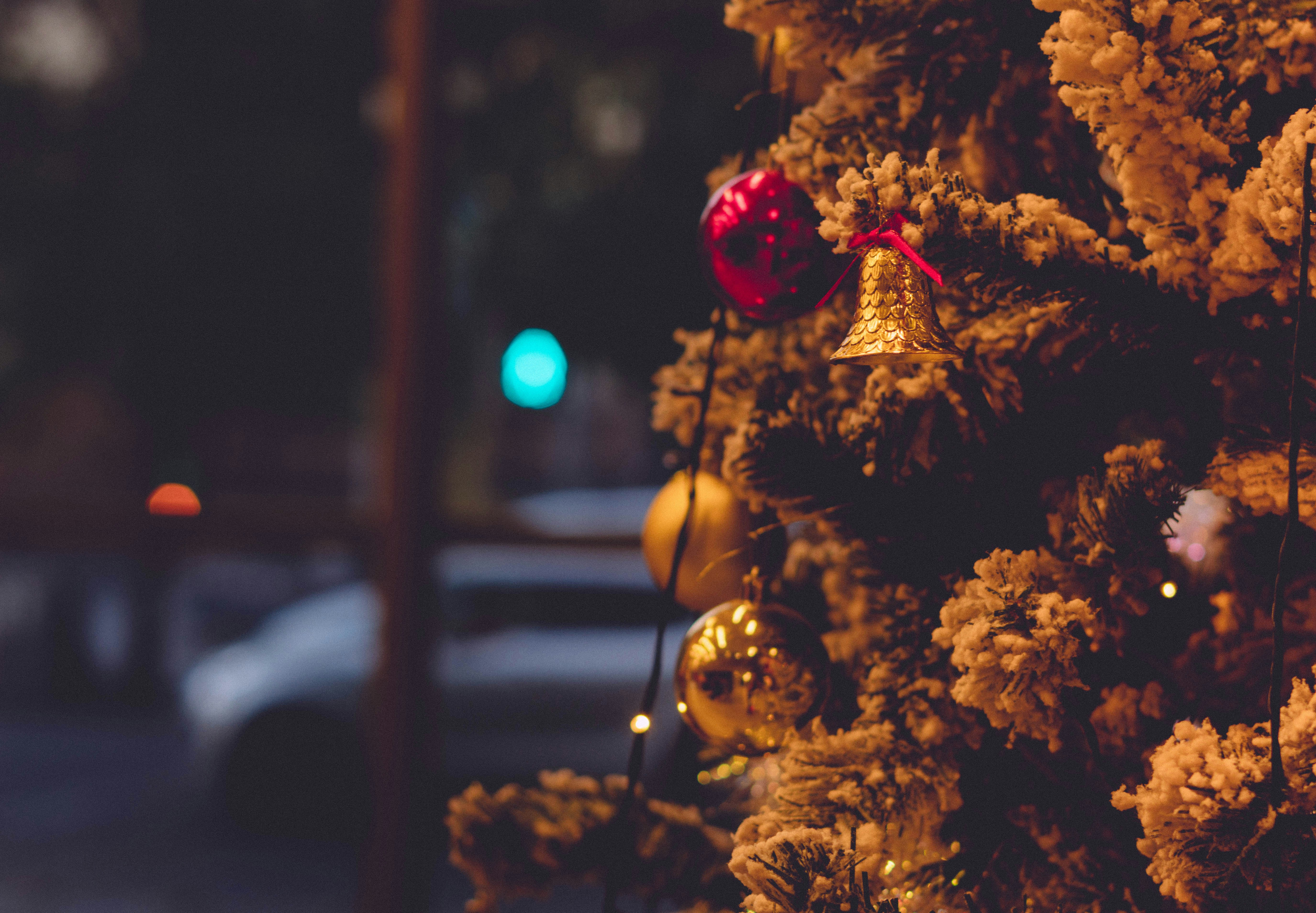 Close-up of a Christmas tree adorned with colorful ornaments against a blurred city street backdrop.