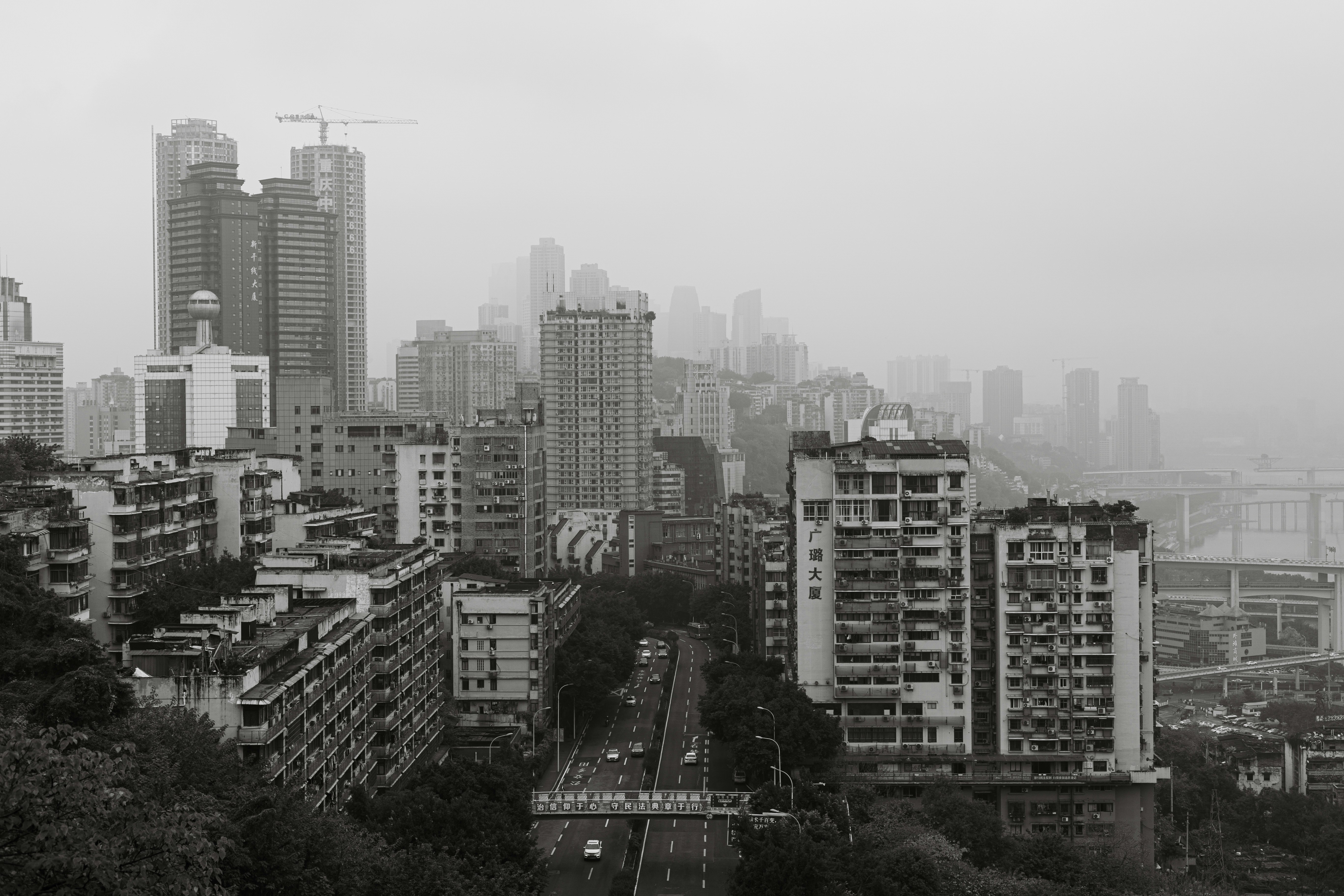 A fog-laden cityscape showcasing towering skyscrapers and bustling roads, captured in black and white. The atmosphere conveys a sense of mystery and depth.