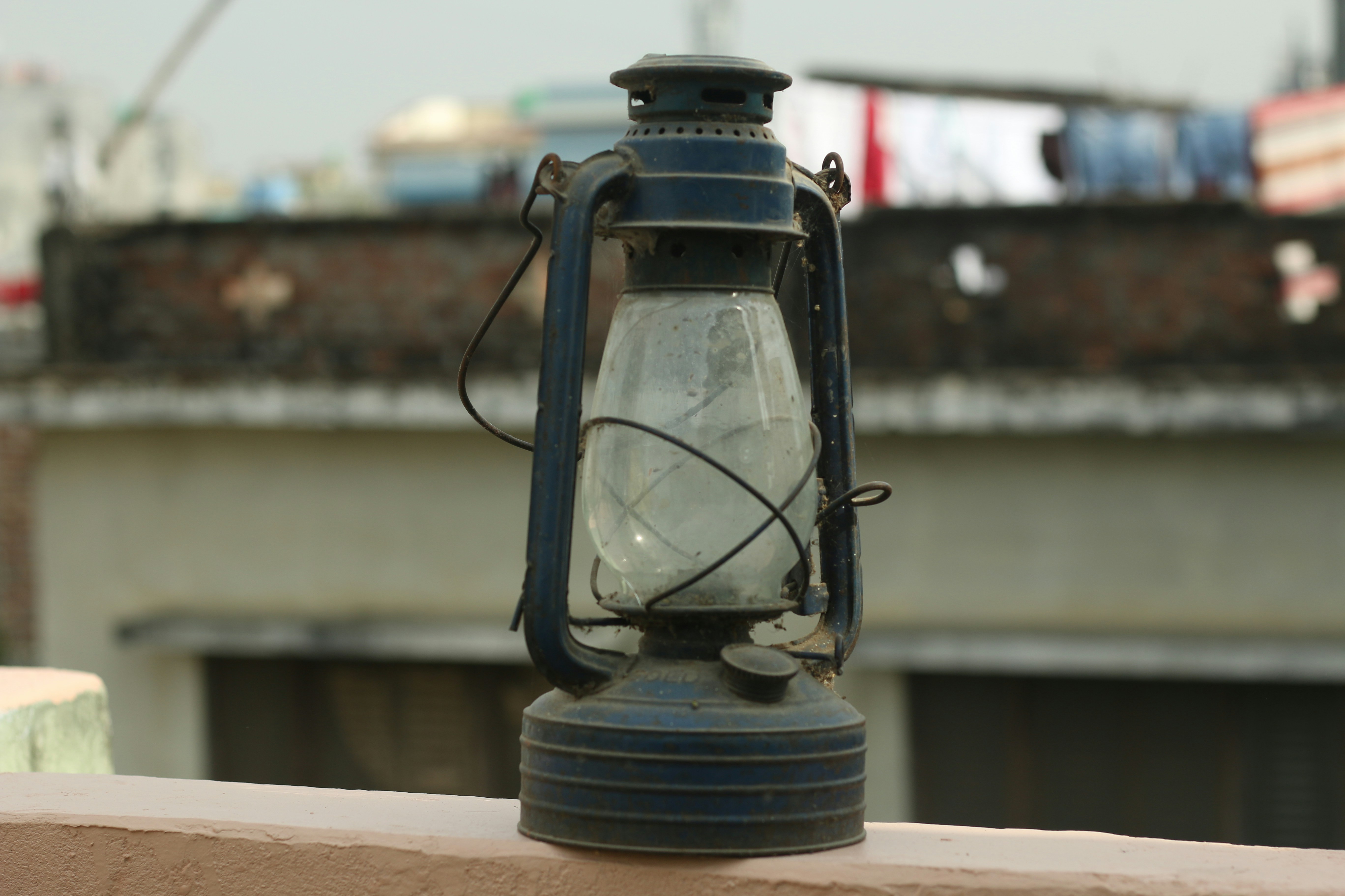 Weathered lantern on a rooftop ledge with blurred urban backdrop.