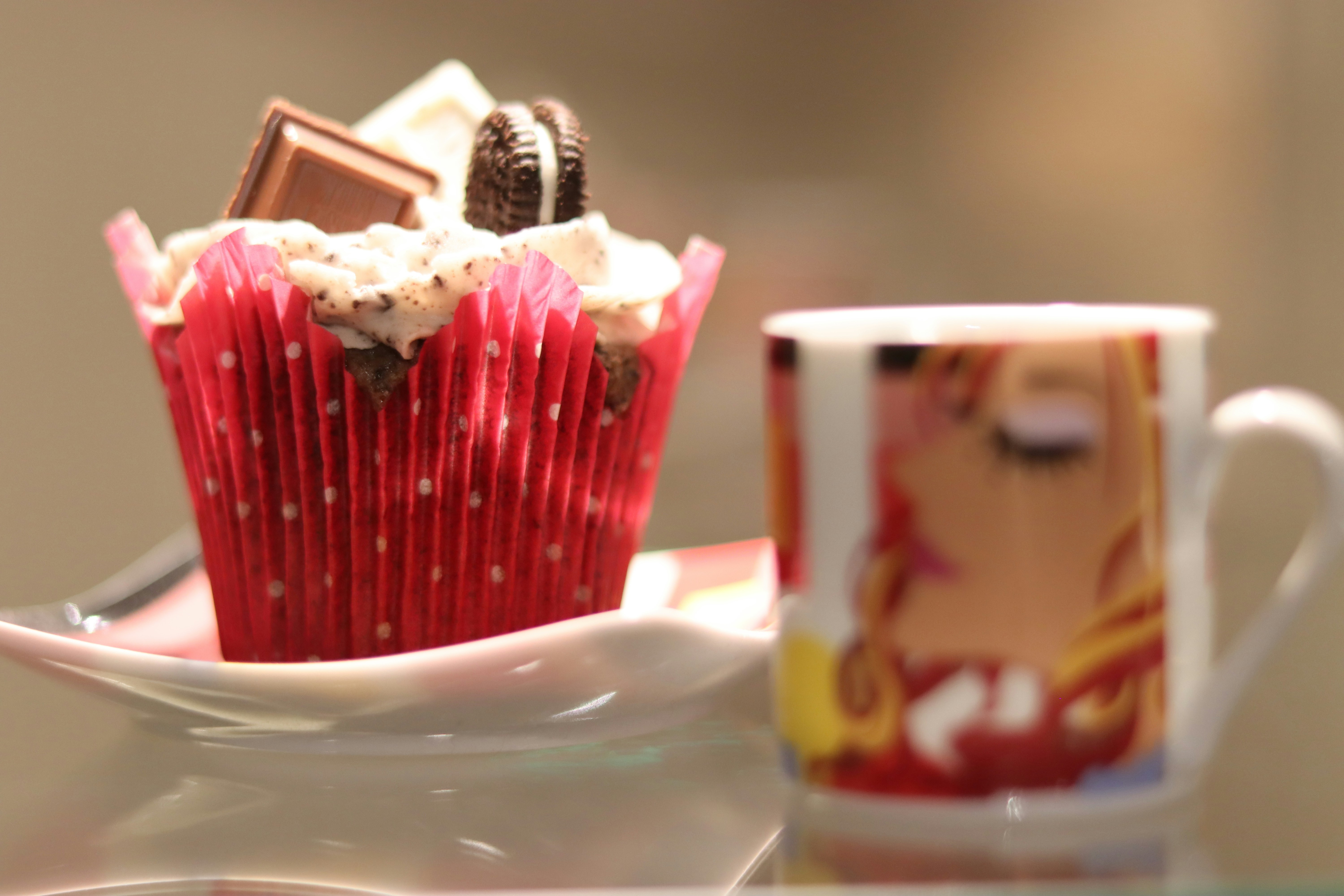 Oreo-Crumble Cupcake on a White Plate, Framed by a Soft Mug Blur