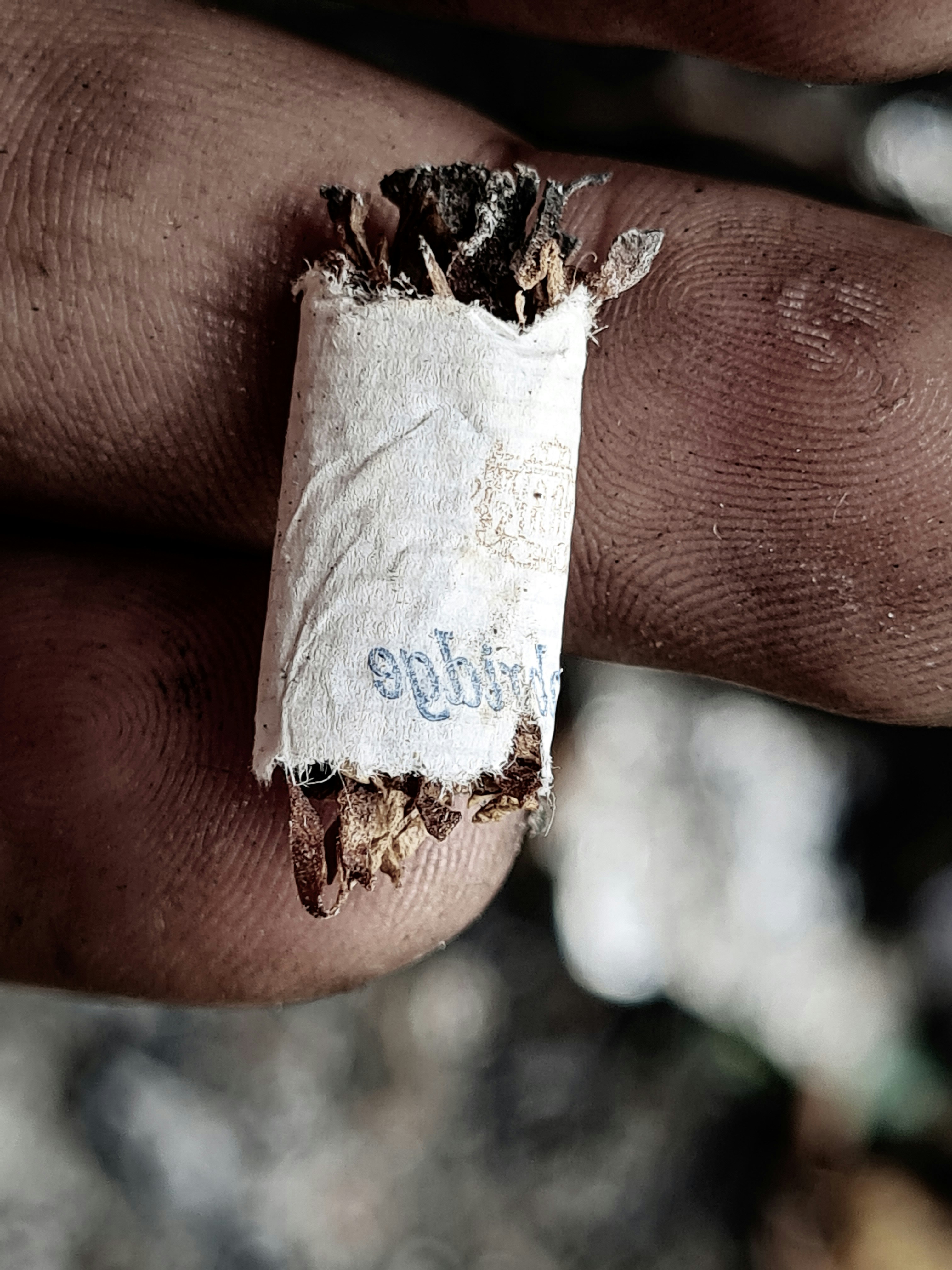 Close-up of a hand holding a cigarette butt, with focus on the textured skin and tobacco remnants.