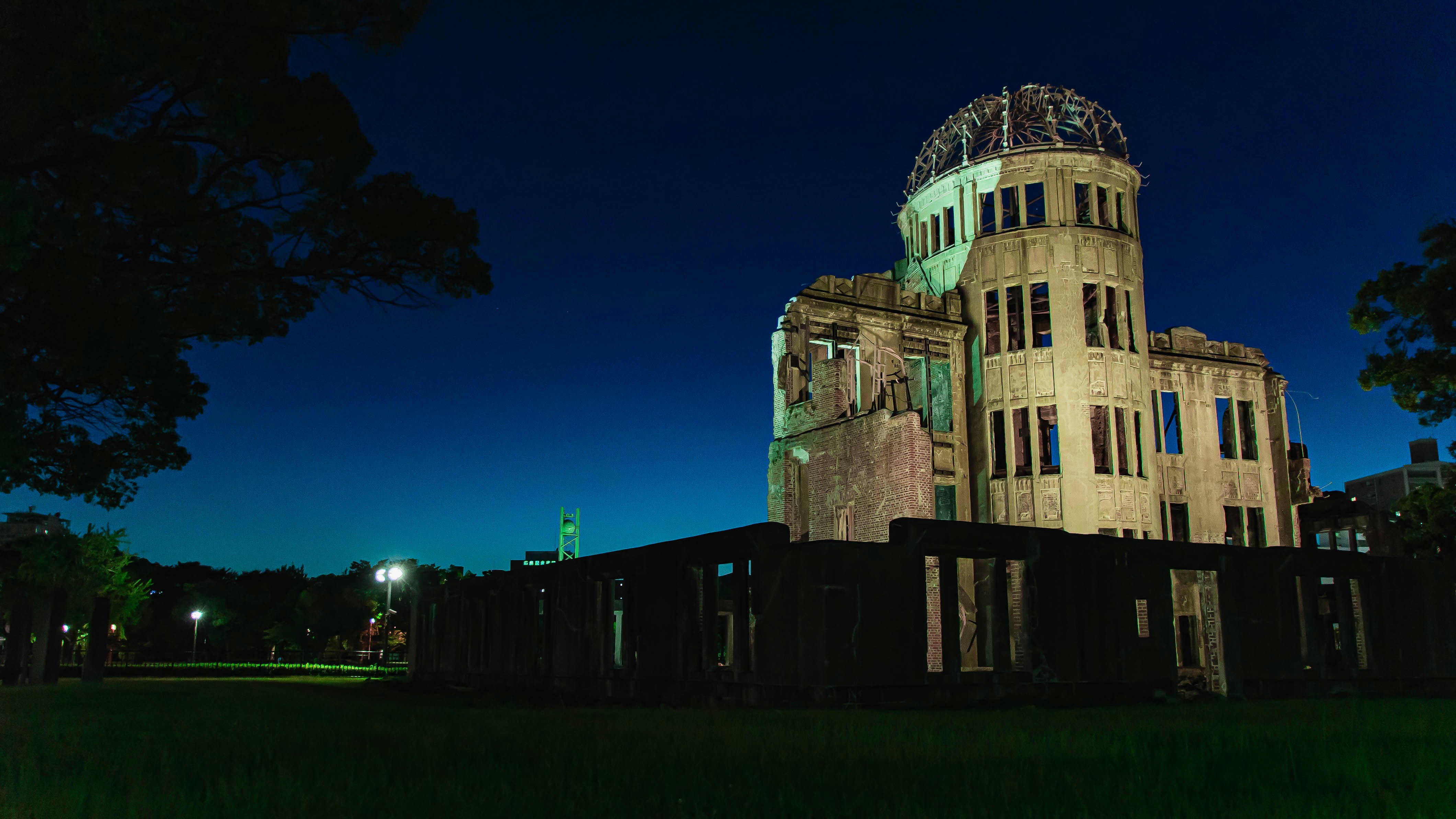 Historic building with a dome lit up at night, surrounded by dark trees and a deep blue sky.