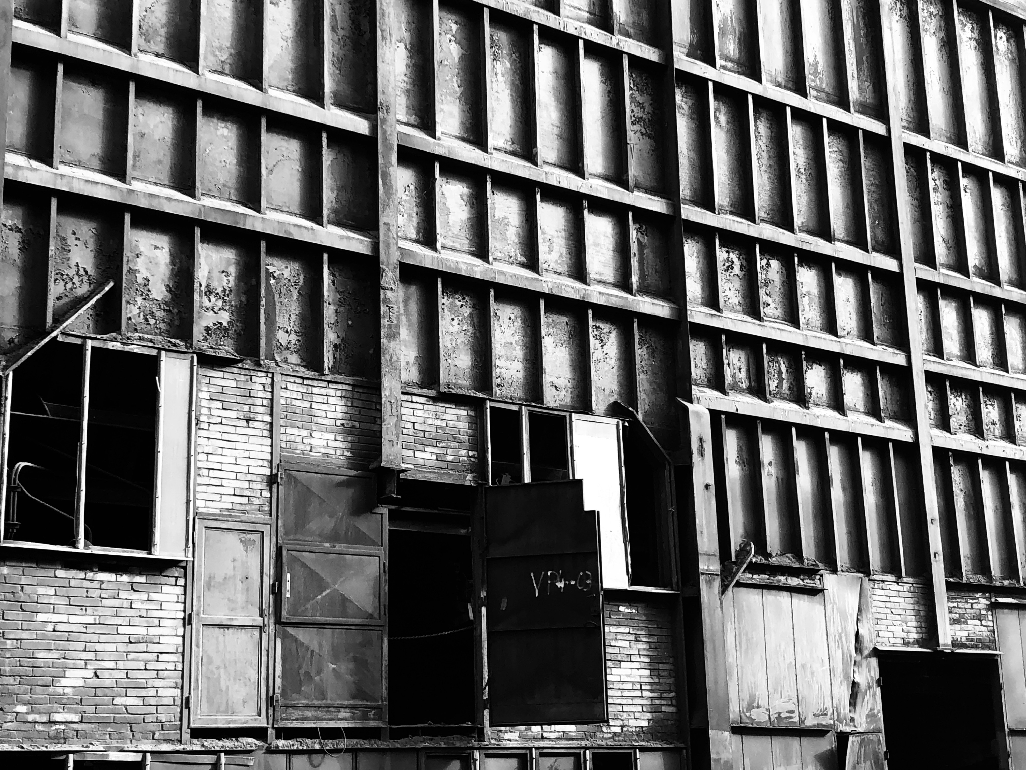 Weathered industrial building showcasing a series of broken doors and windows, highlighting the passage of time and abandonment.