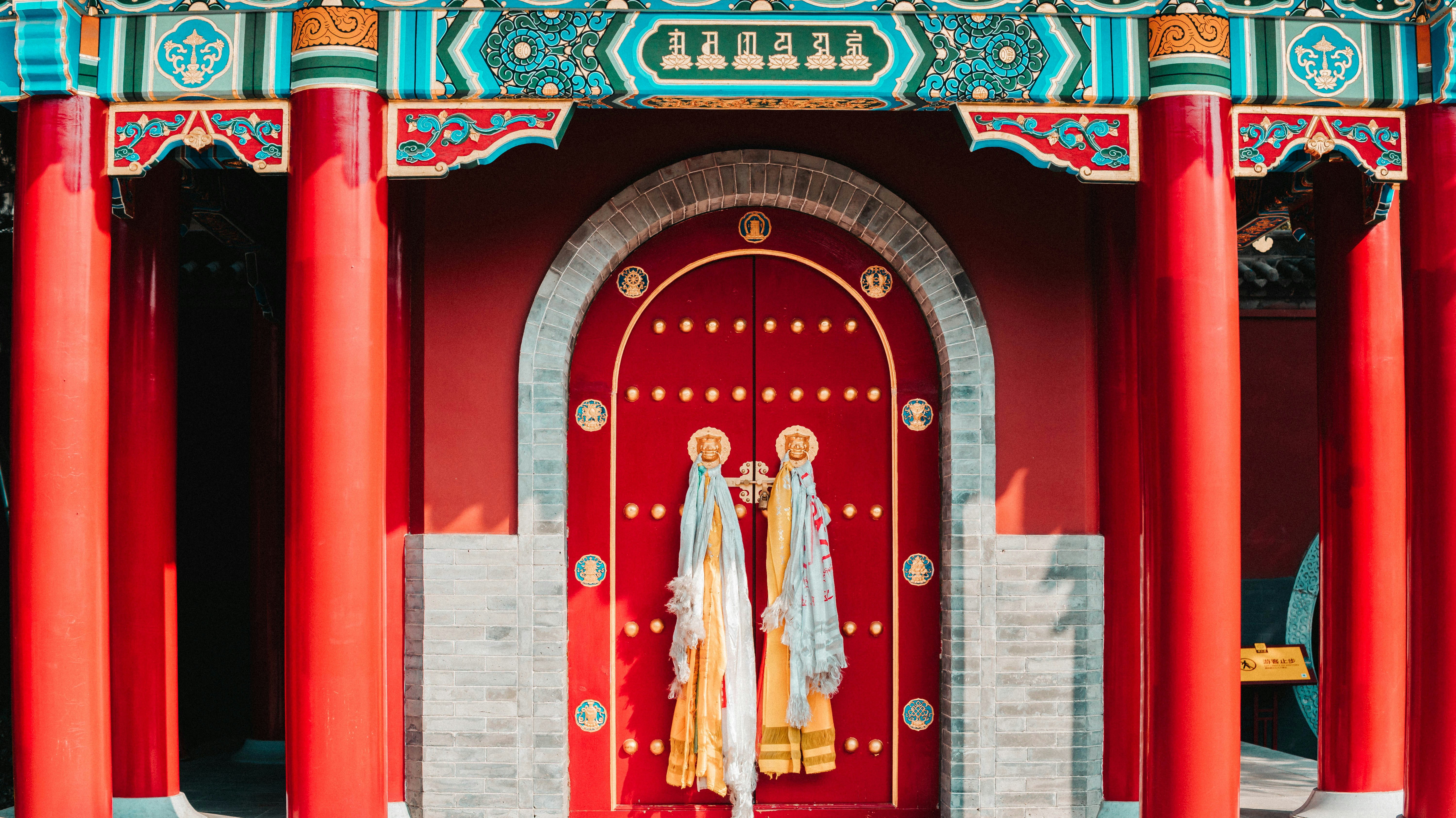 Intricately designed red doors adorned with golden knobs and traditional garments hanging, framed by vibrant pillars and ornate architecture.