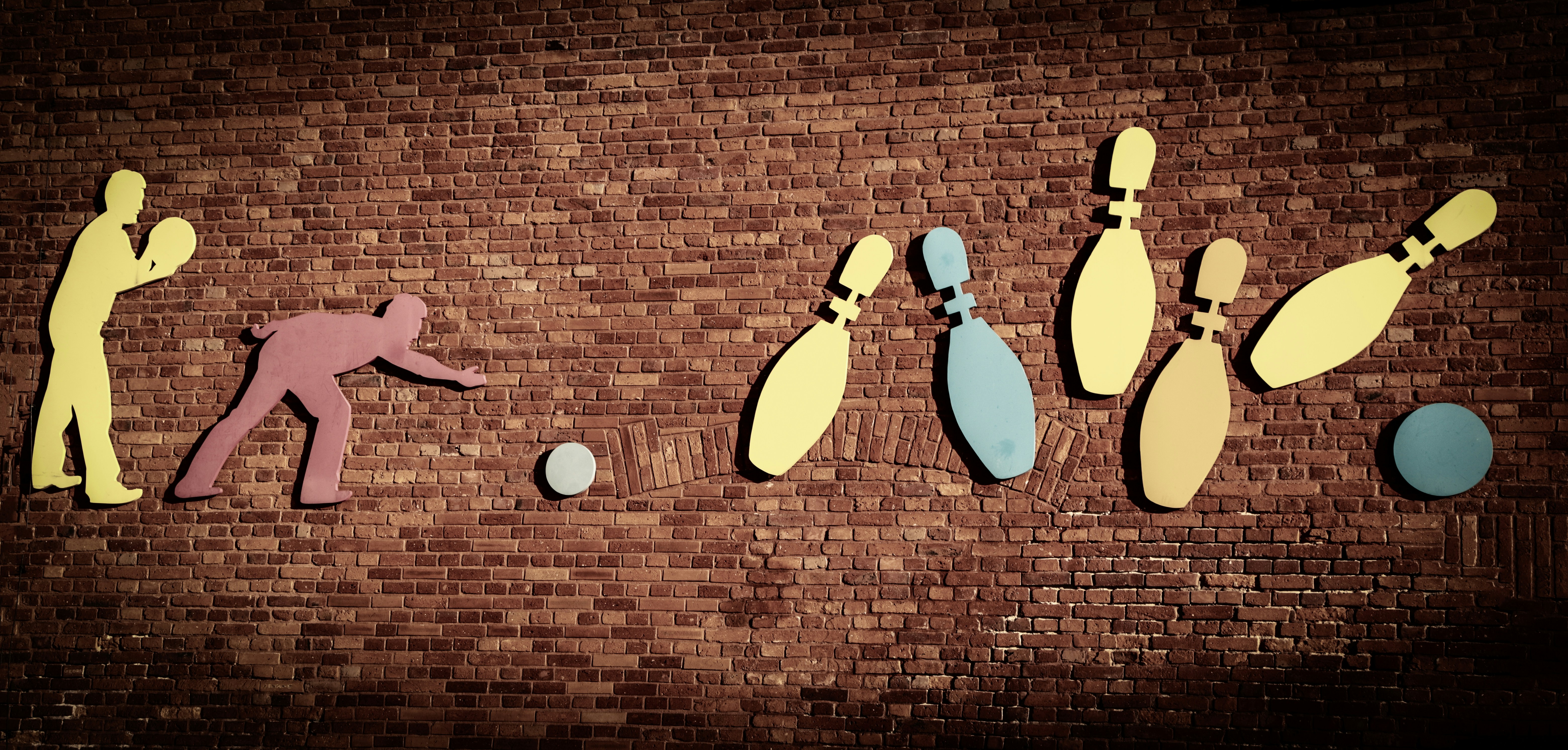 a brick wall with paper cutouts of people playing a game of bowling