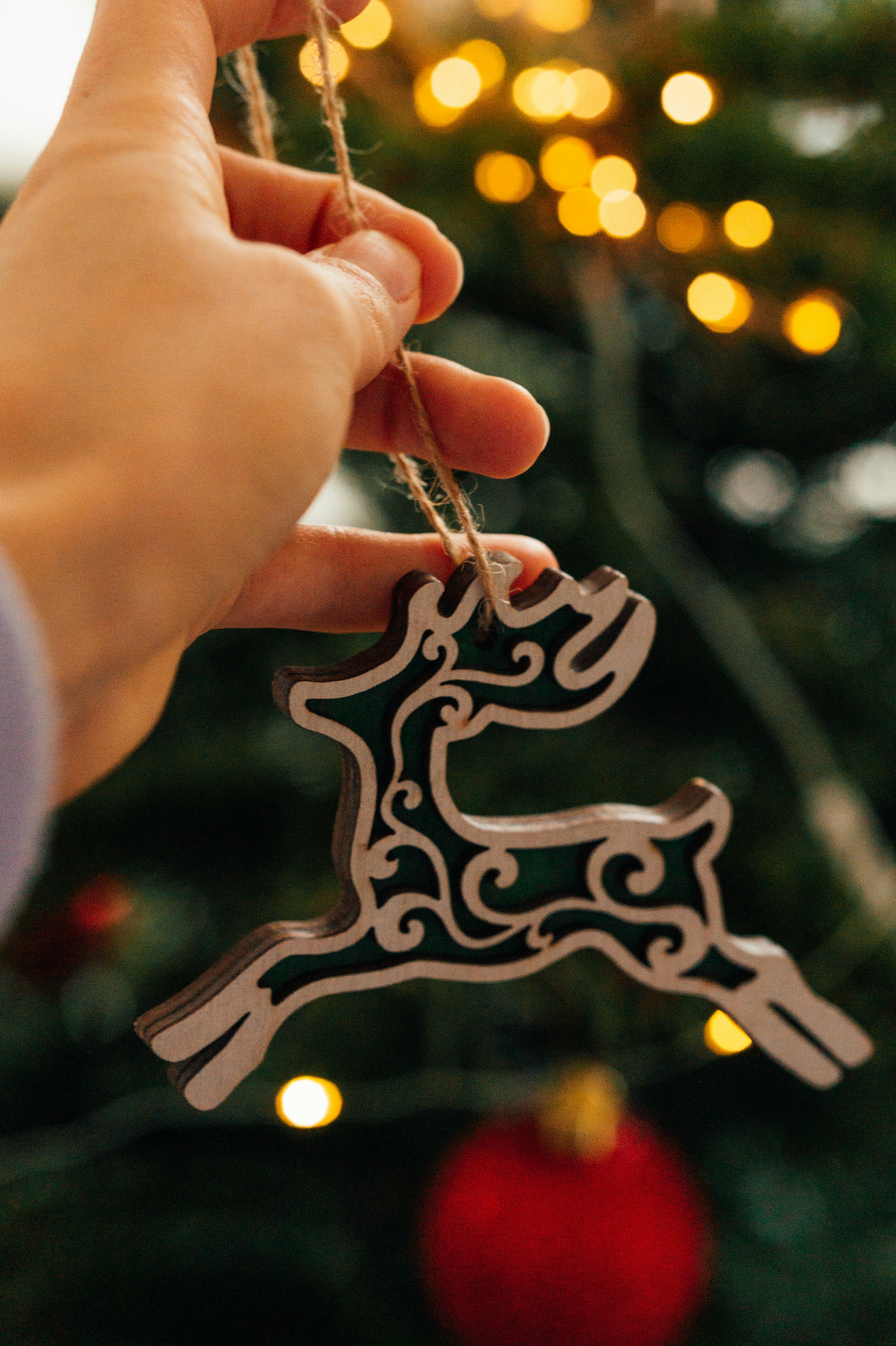 A Wooden Reindeer Ornament Suspended Against Soft Christmas Lights