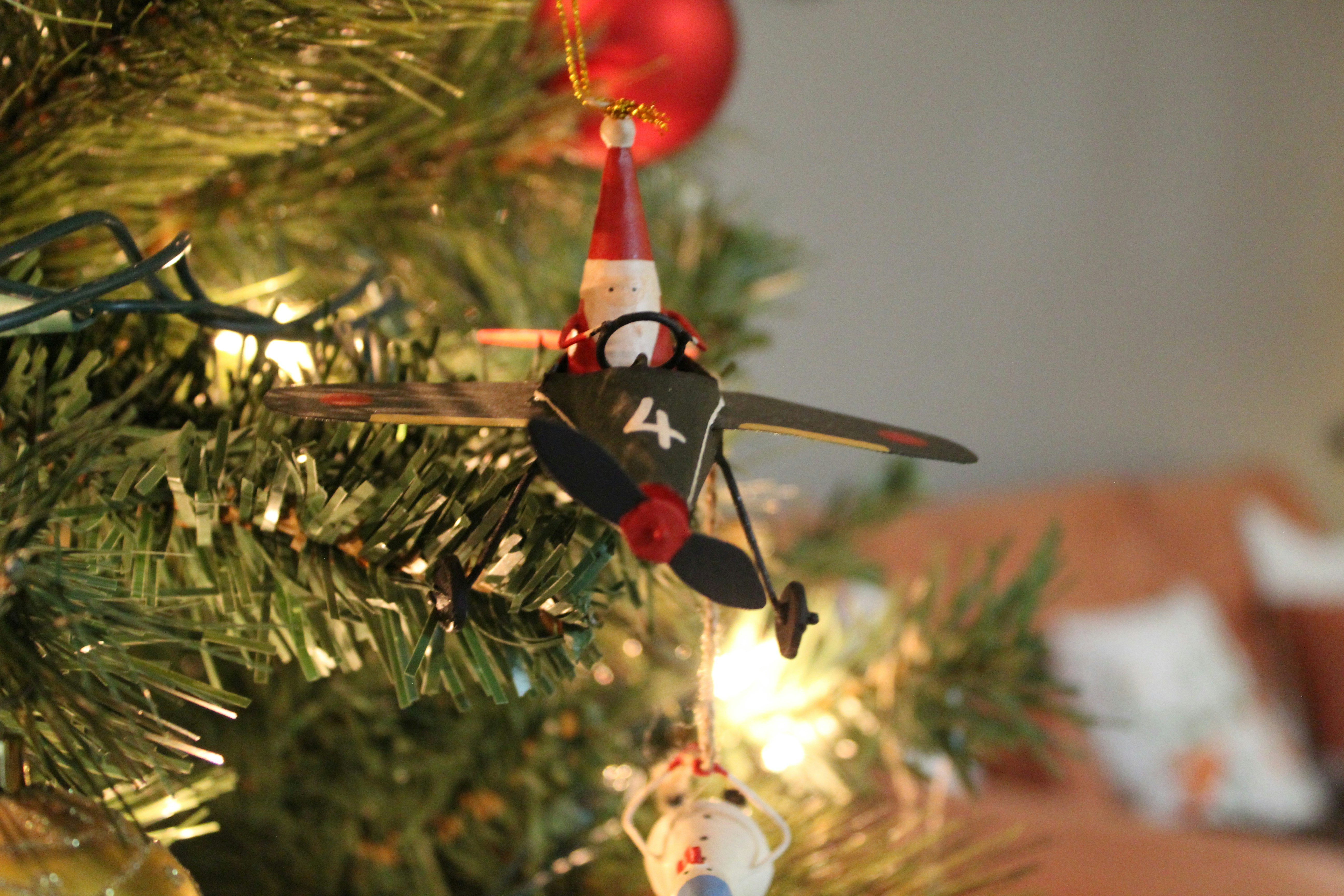 A whimsical airplane ornament adorned with a Santa hat, nestled among the branches of a Christmas tree, illuminated by soft lights.
