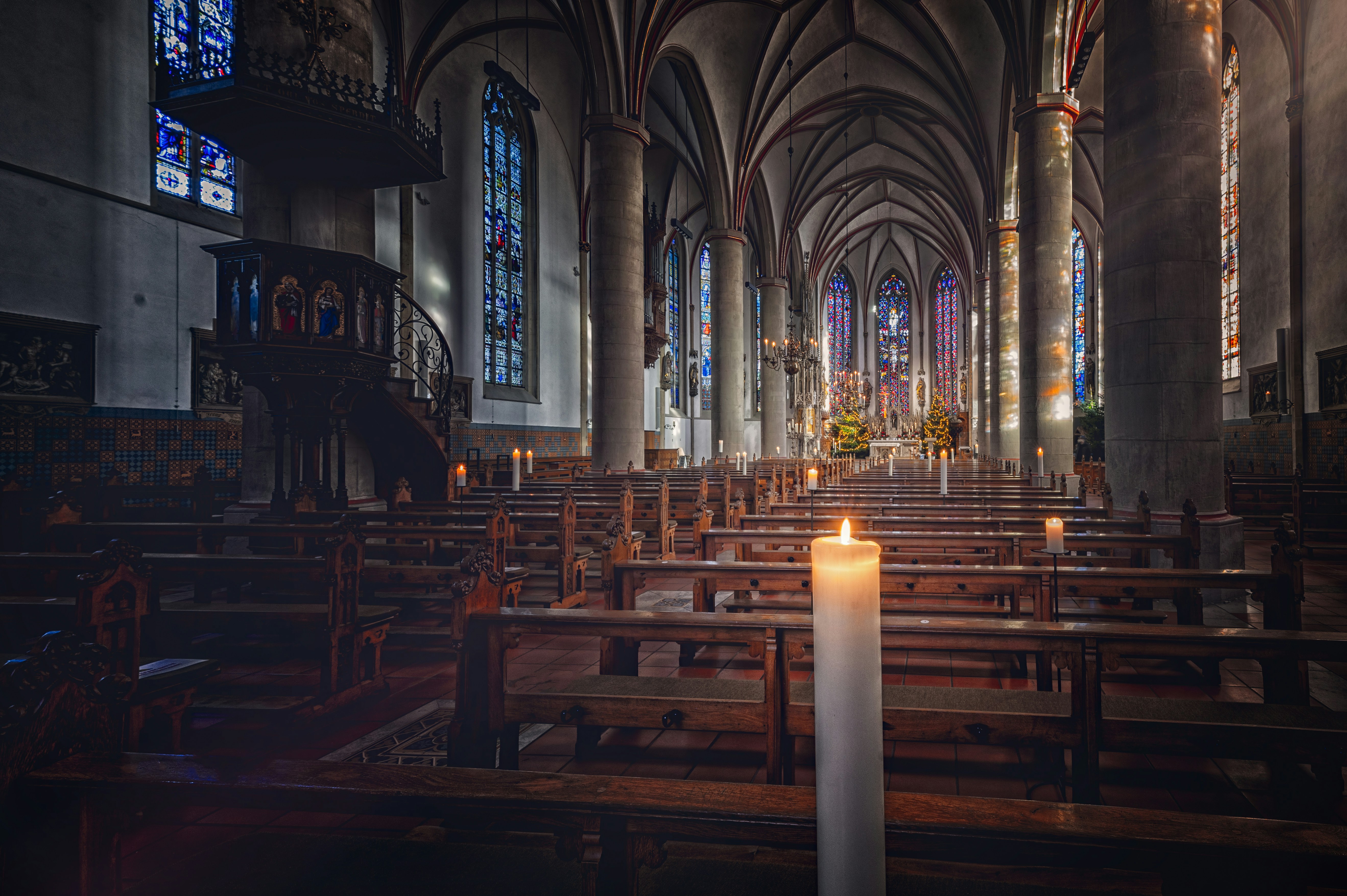 Softly glowing candles illuminate the tranquil interior of a church, highlighting intricate stained glass windows and wooden pews.