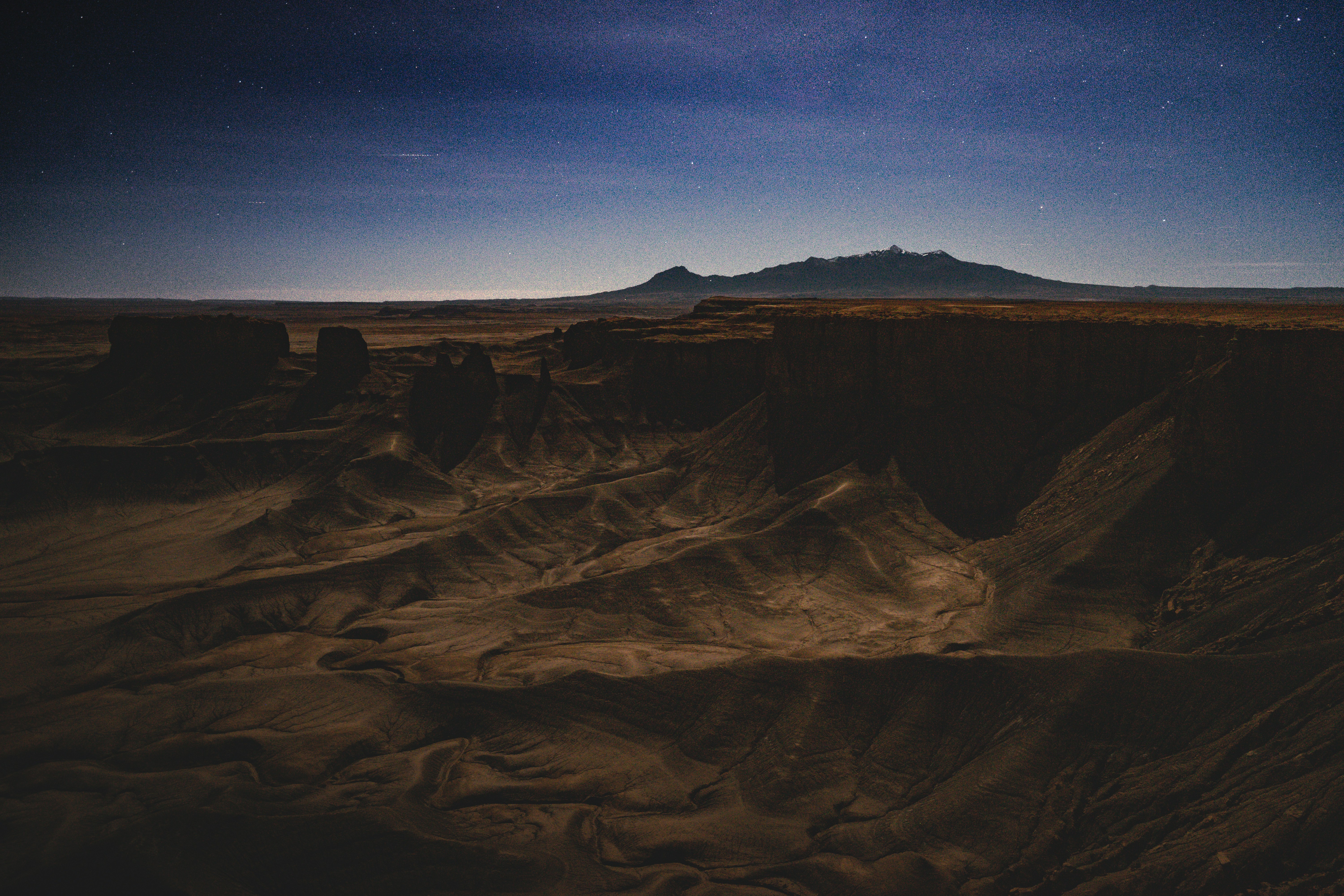 Moonlit desert landscape revealing intricate sand patterns and distant mountains under a starry sky.