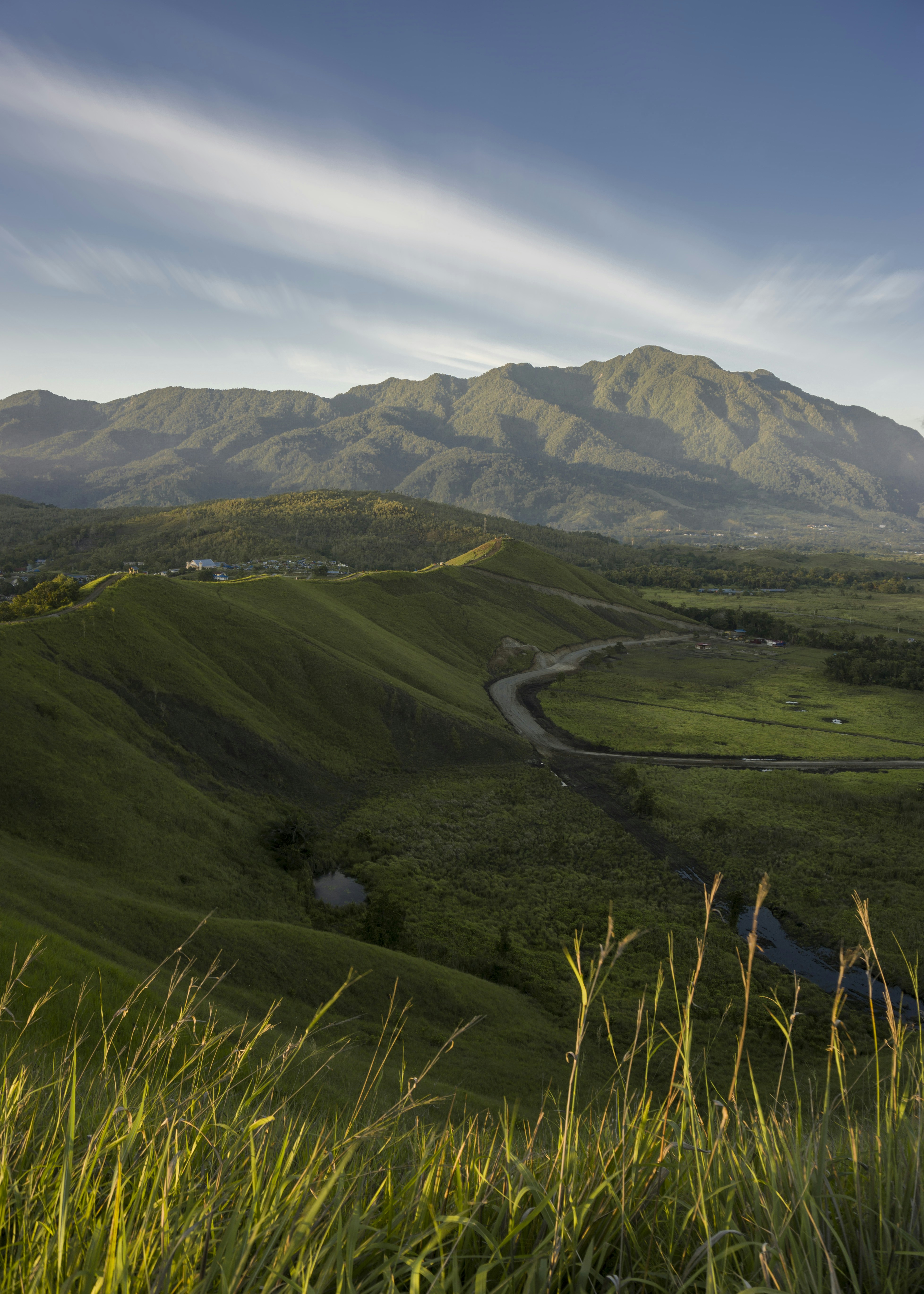 Lush rolling hills meet a winding river beneath a majestic mountain range, capturing the serene beauty of nature at dusk.