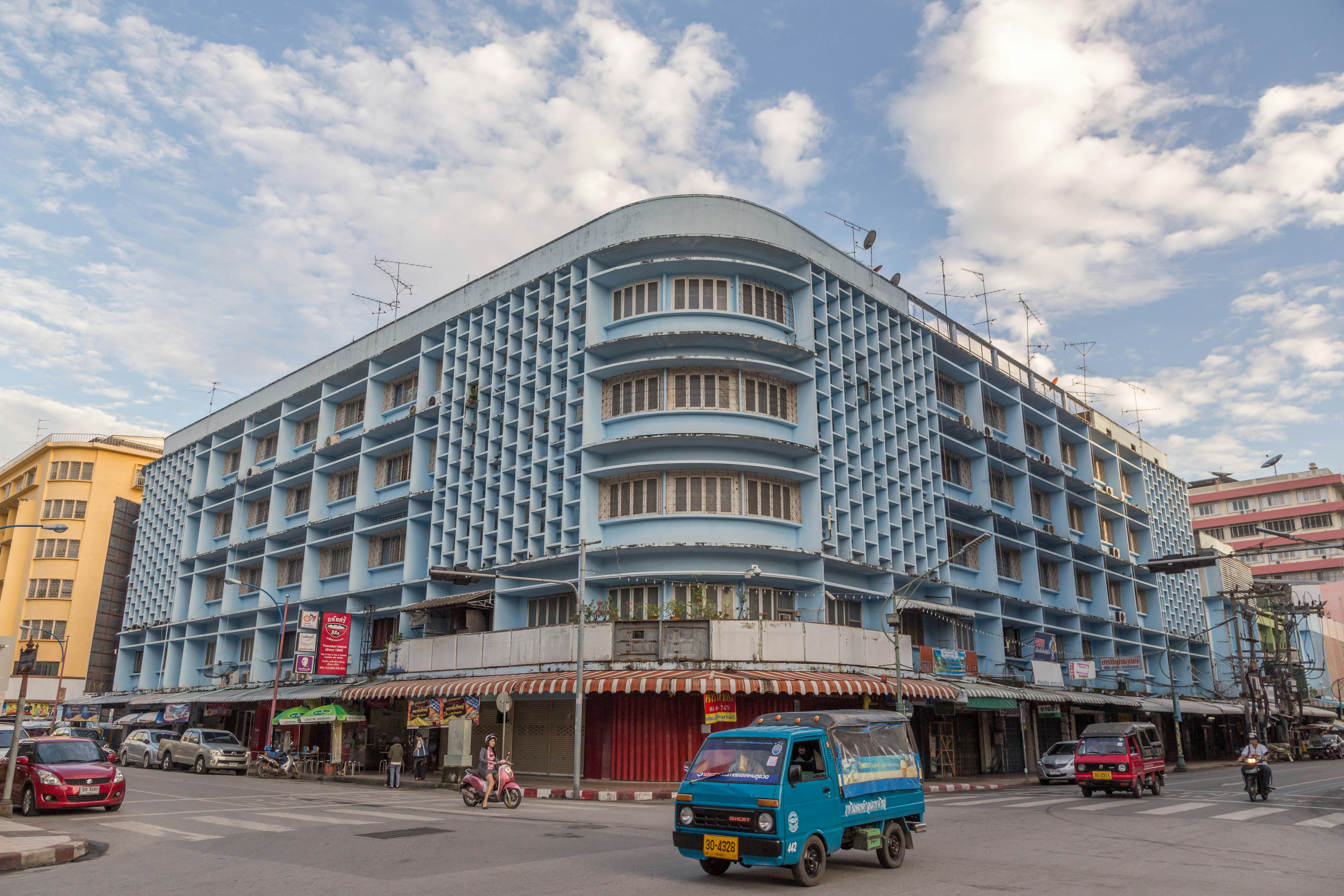 Geometric blue building with unique façade design, surrounded by bustling streets and vehicles. The scene captures the essence of urban life.