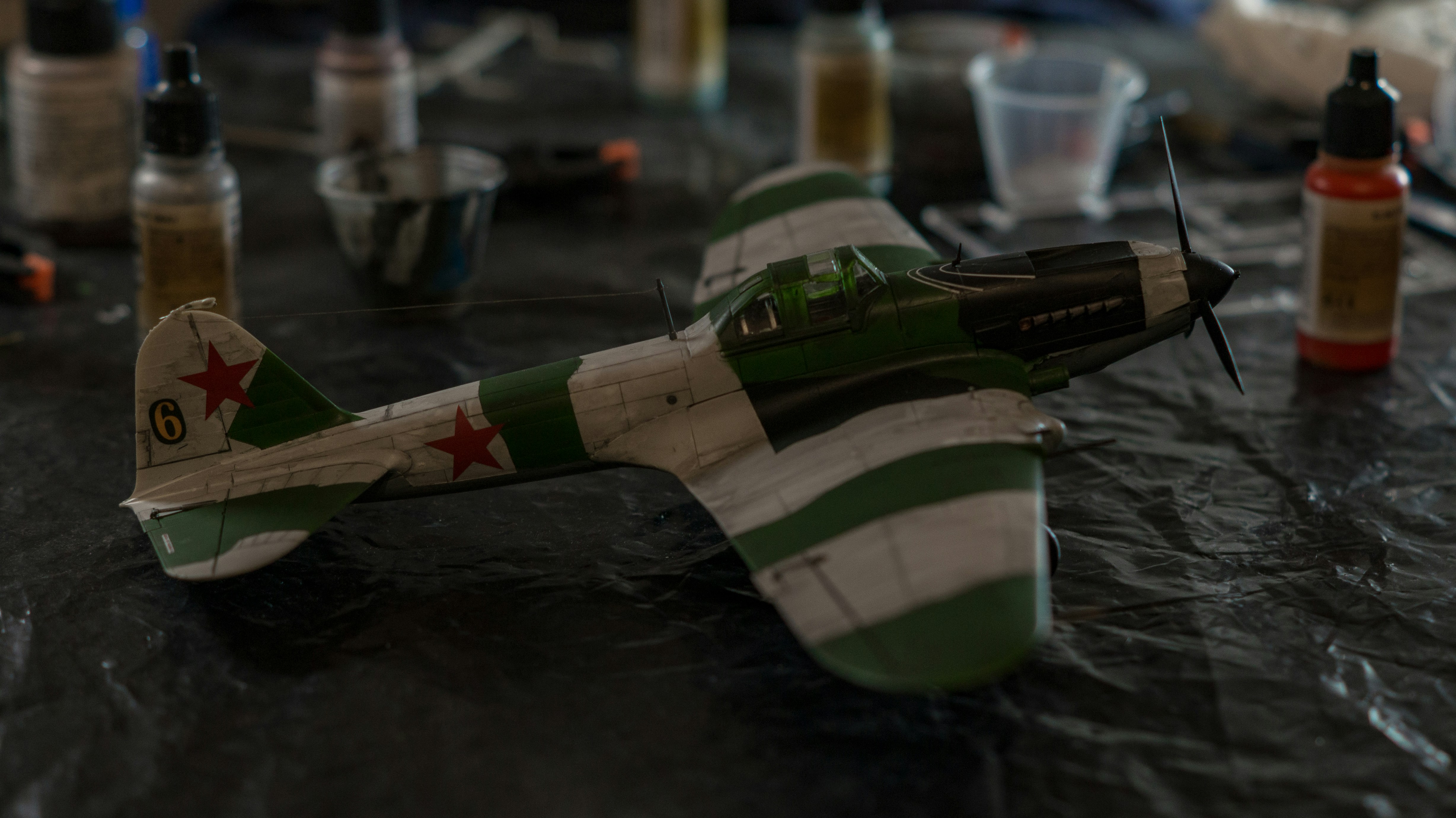 Paint-Splattered Ambition: A Green-and-White Warplane Model in a Cluttered Workshop