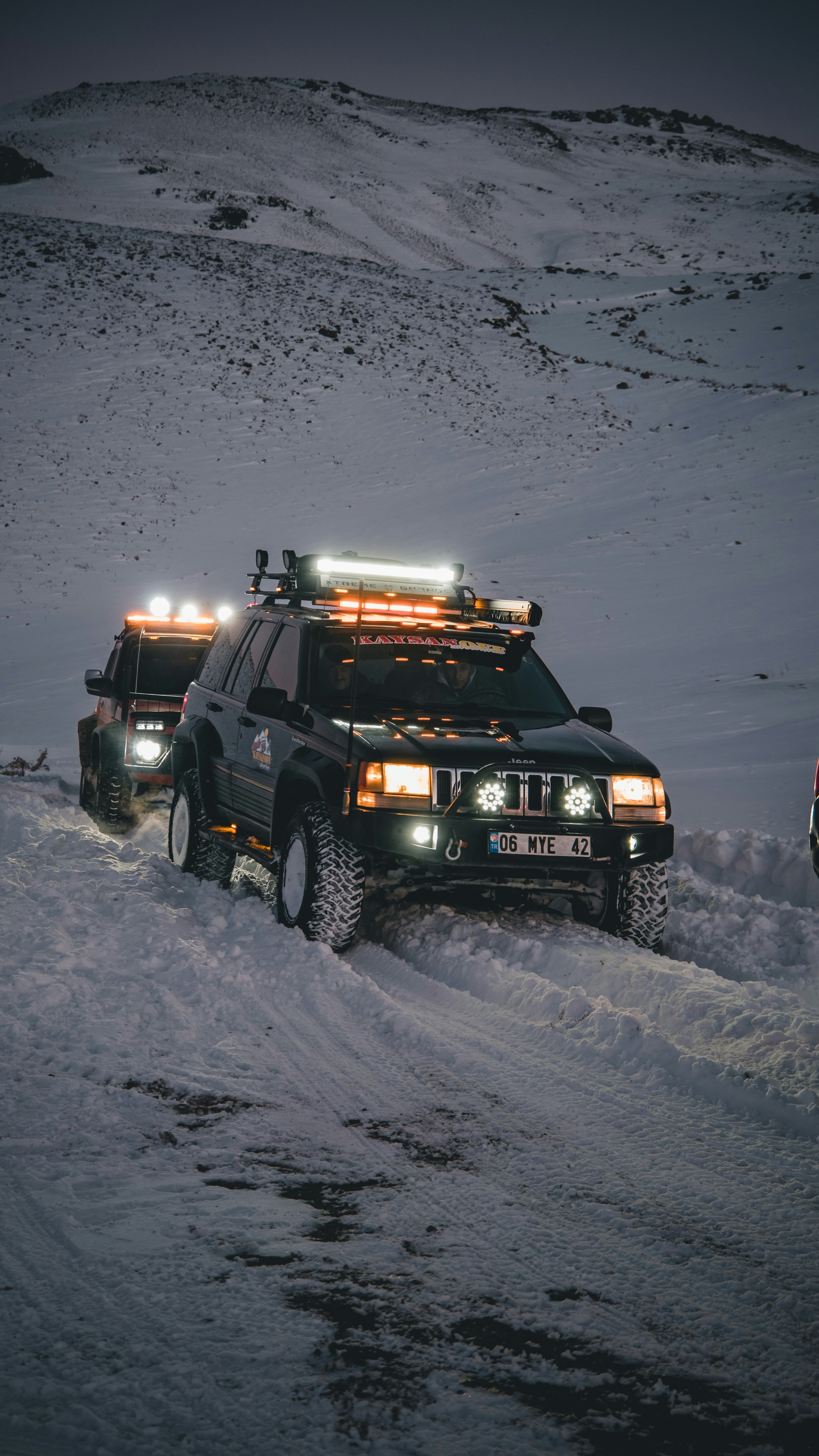 Luminous Convoy on a Snowbound Pass Beneath a Dark Ridge