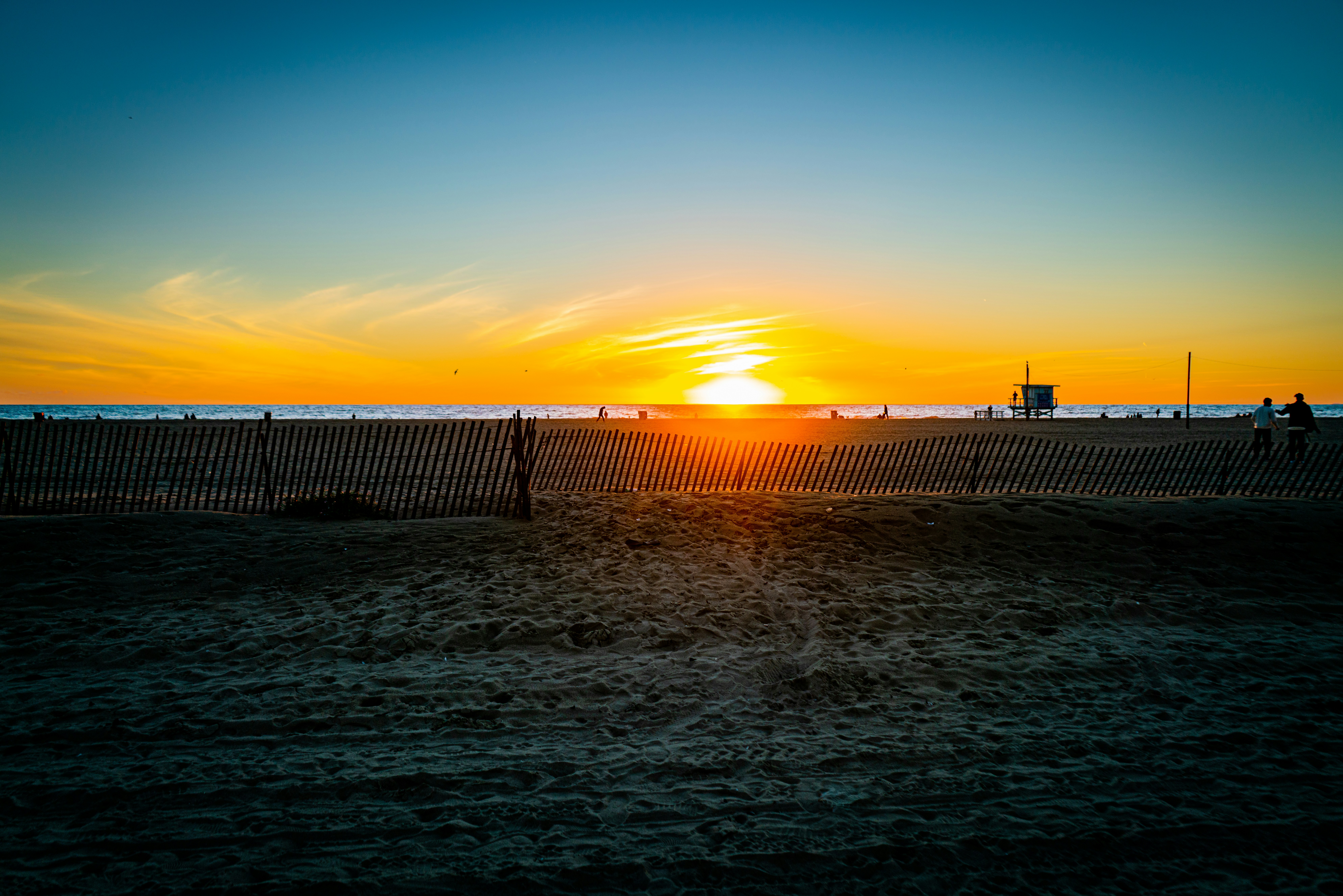 Horizon Ember: Sunset Through a Fence-Lined Beach