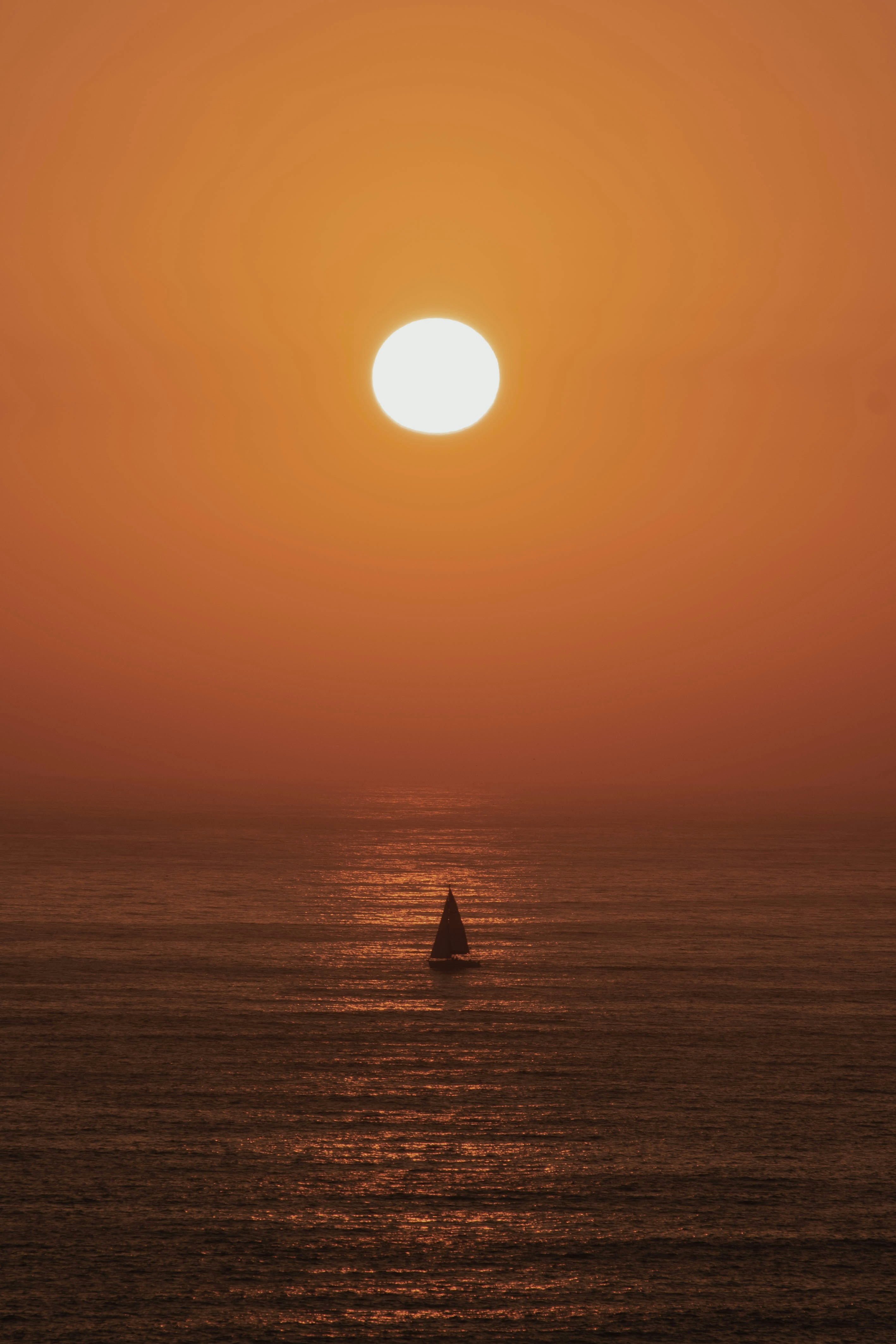 Crimson Horizon: solitary sailboat at orange dusk