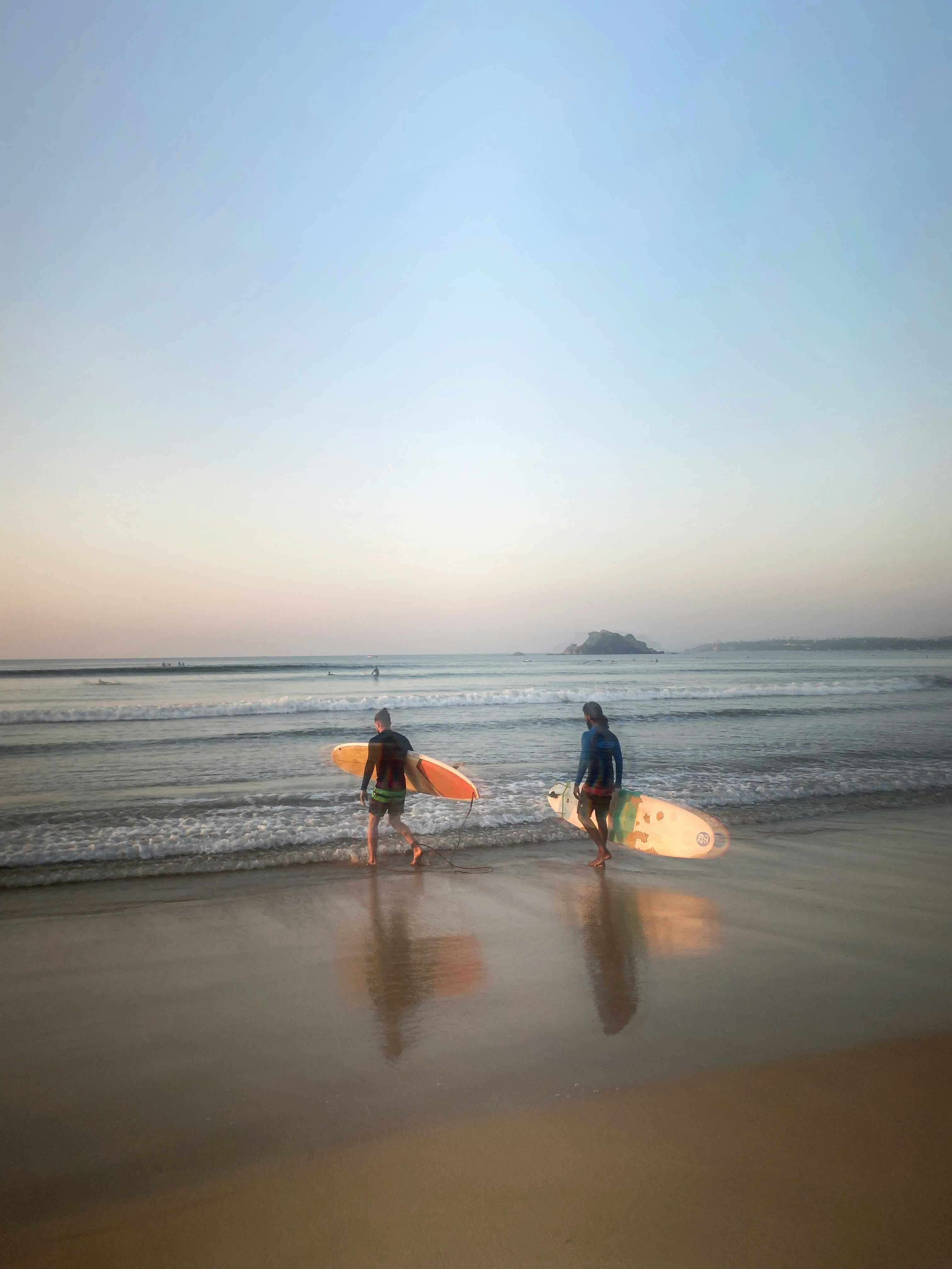 Dusk on the Shore: Two Surfers Carrying Boards Across Tidal Reflections