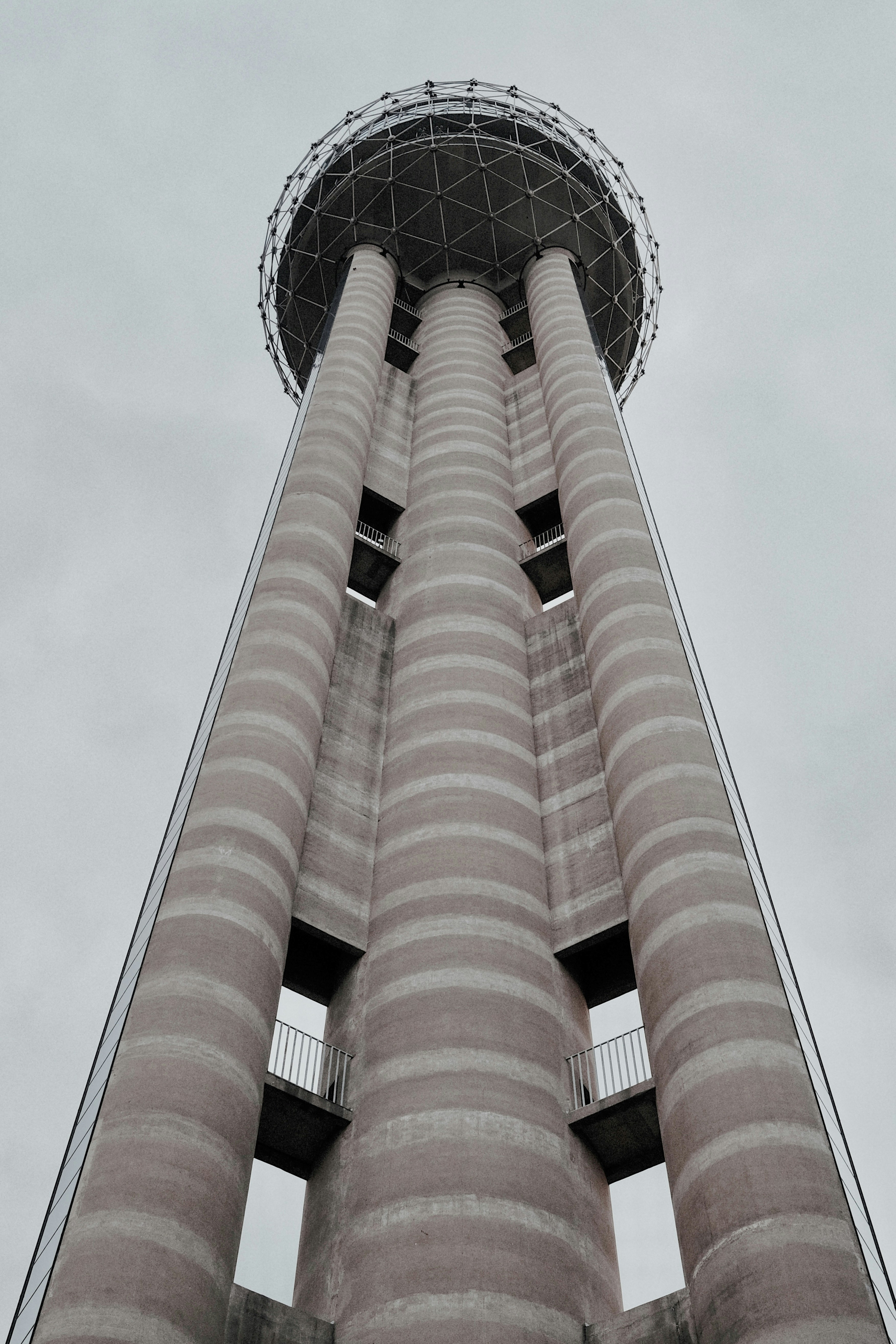 A towering concrete structure rises against a cloudy sky, showcasing its striped design and geometric patterns. The perspective emphasizes its height and architectural details.