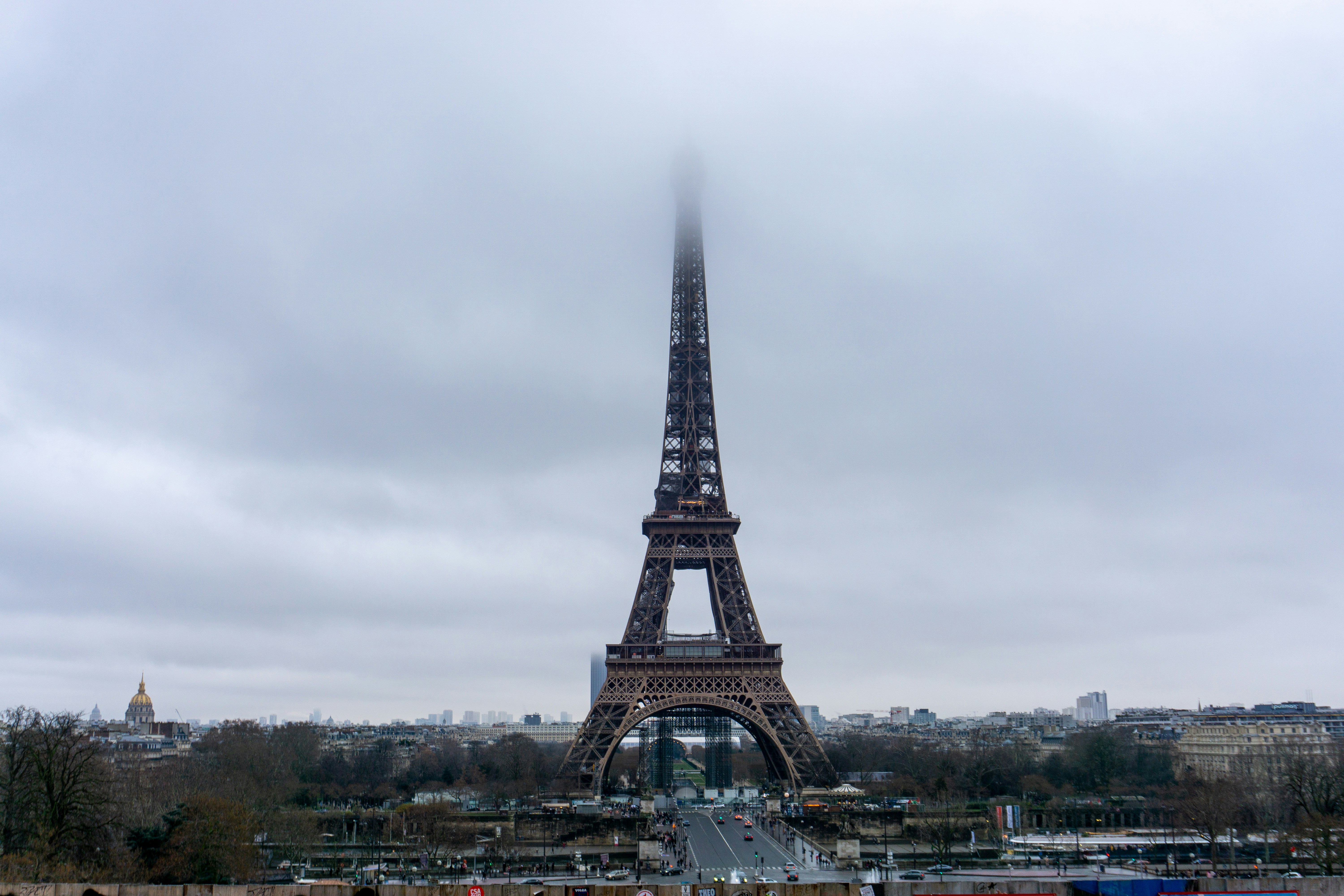 Eiffel Tower partially shrouded in fog, towering over a quiet Paris street. The scene captures a moody atmosphere with soft, diffused light.