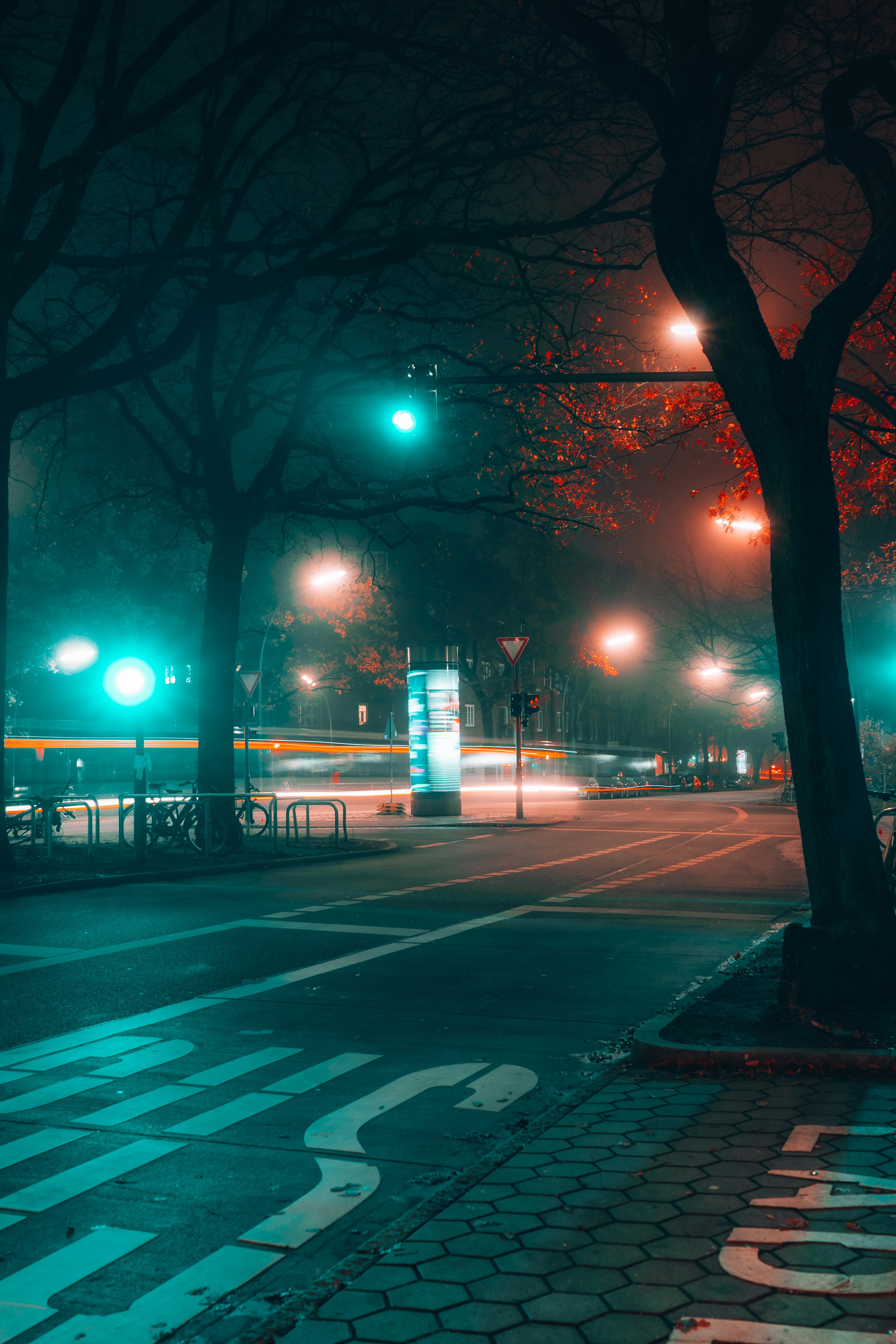 A vibrant urban scene at night, showcasing illuminated traffic signals and blurred vehicle motion amidst foggy conditions. The contrast of colors creates a dynamic atmosphere.