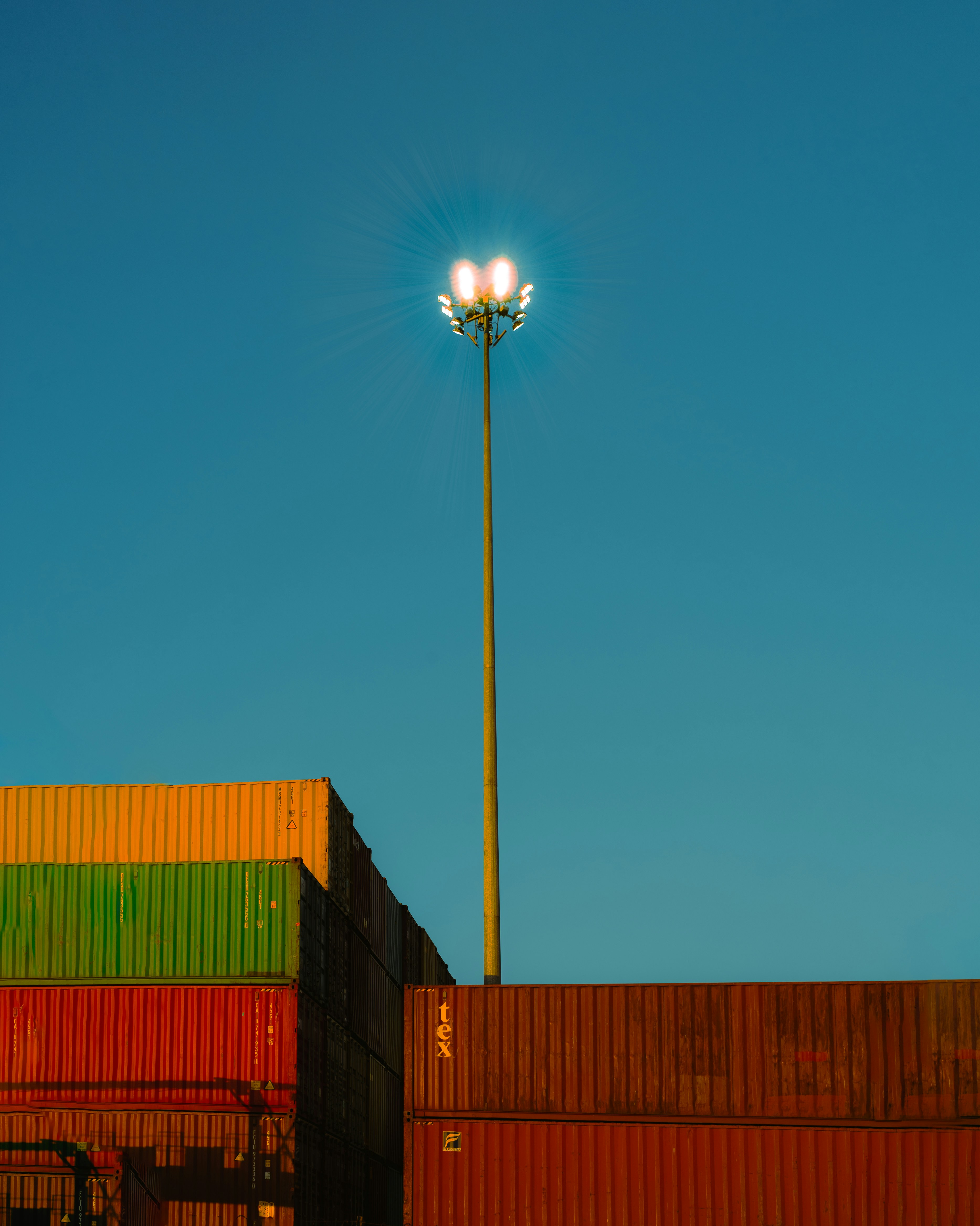 Beacon Above the Container Sea: A Lone Floodlight Over Cargo Blocks