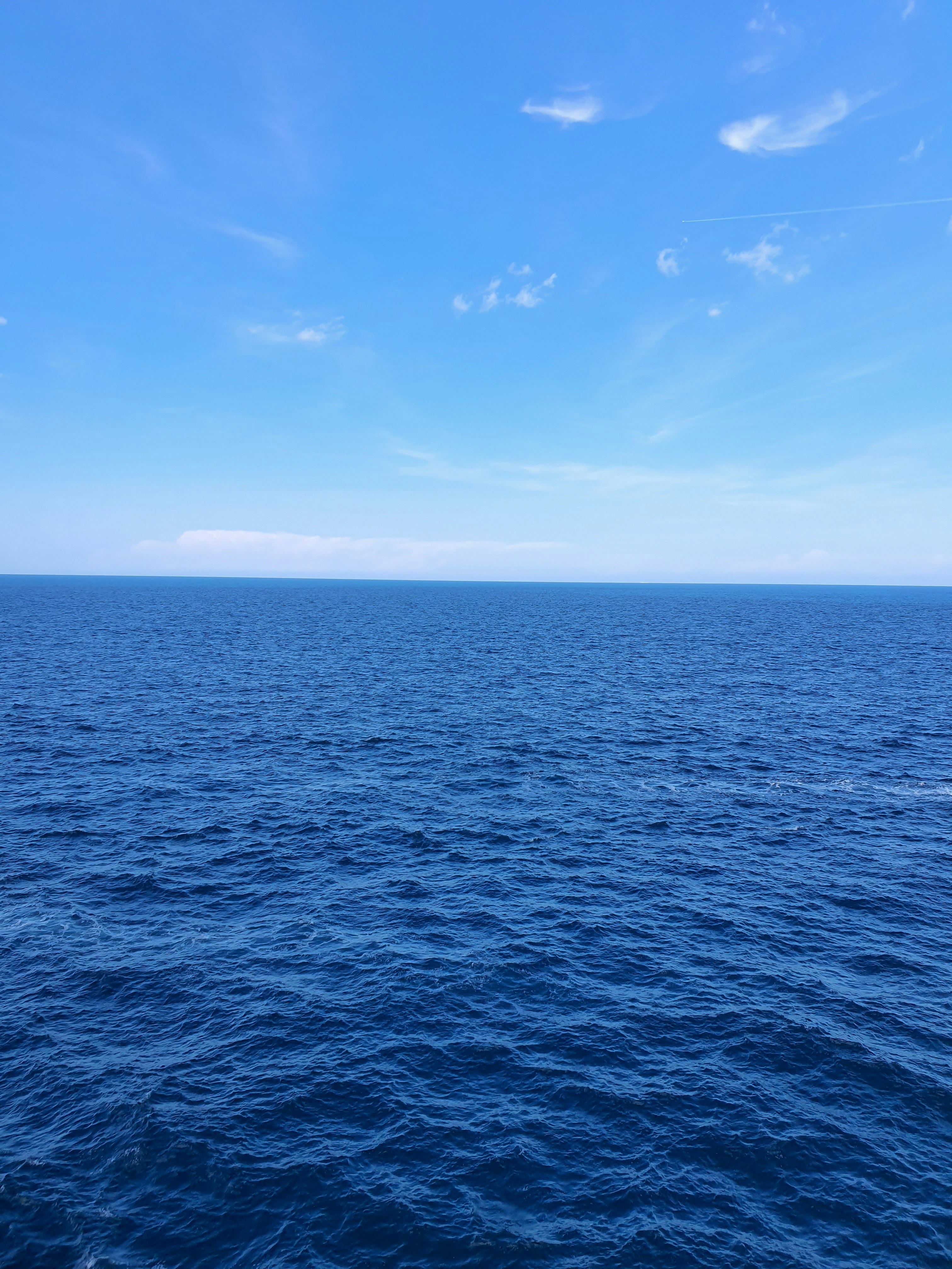 Photograph of a wide blue ocean meeting the horizon under a clear sky, with wispy clouds.