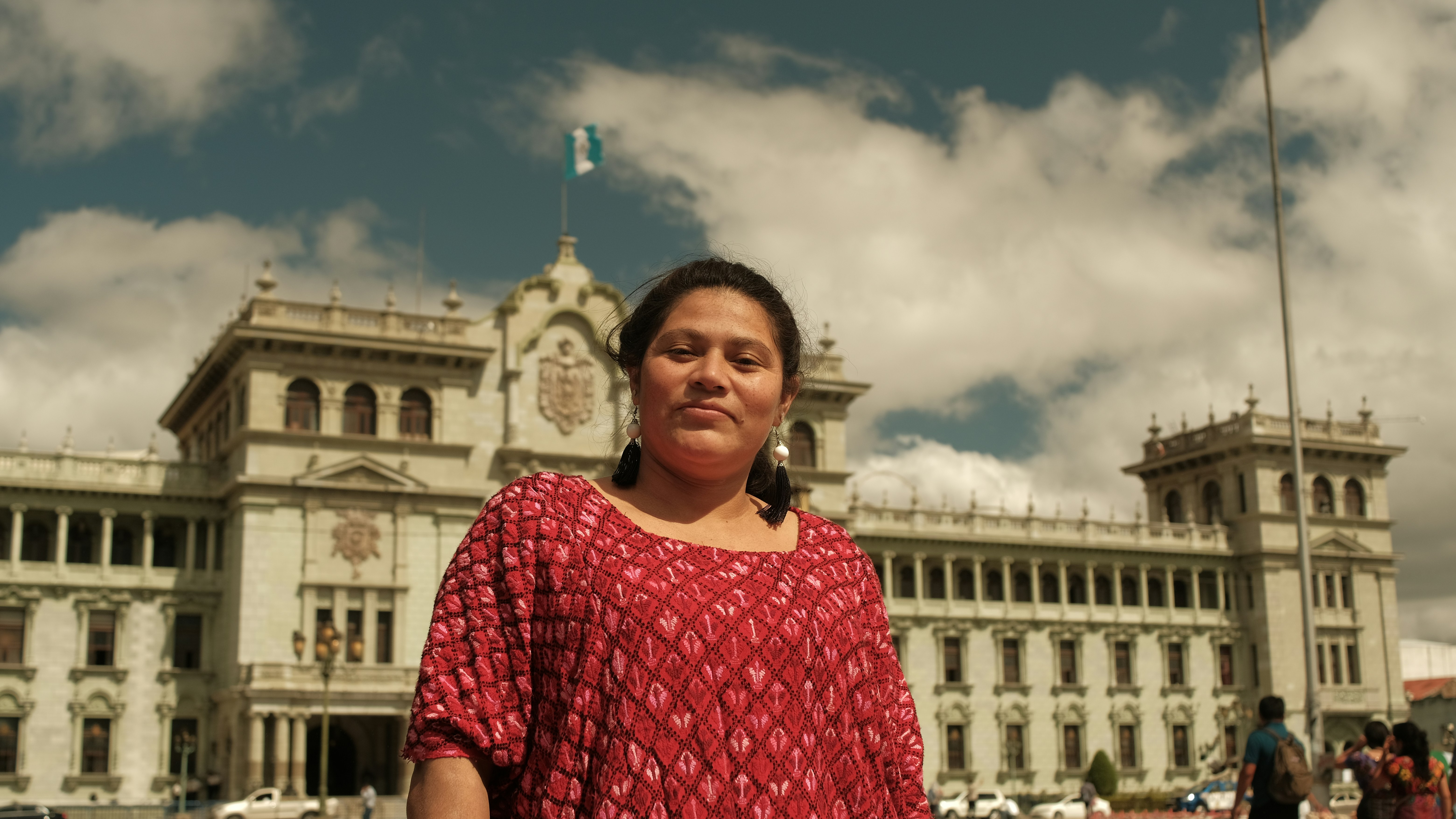 Woman in traditional attire stands before a historic palace under a partly cloudy sky.