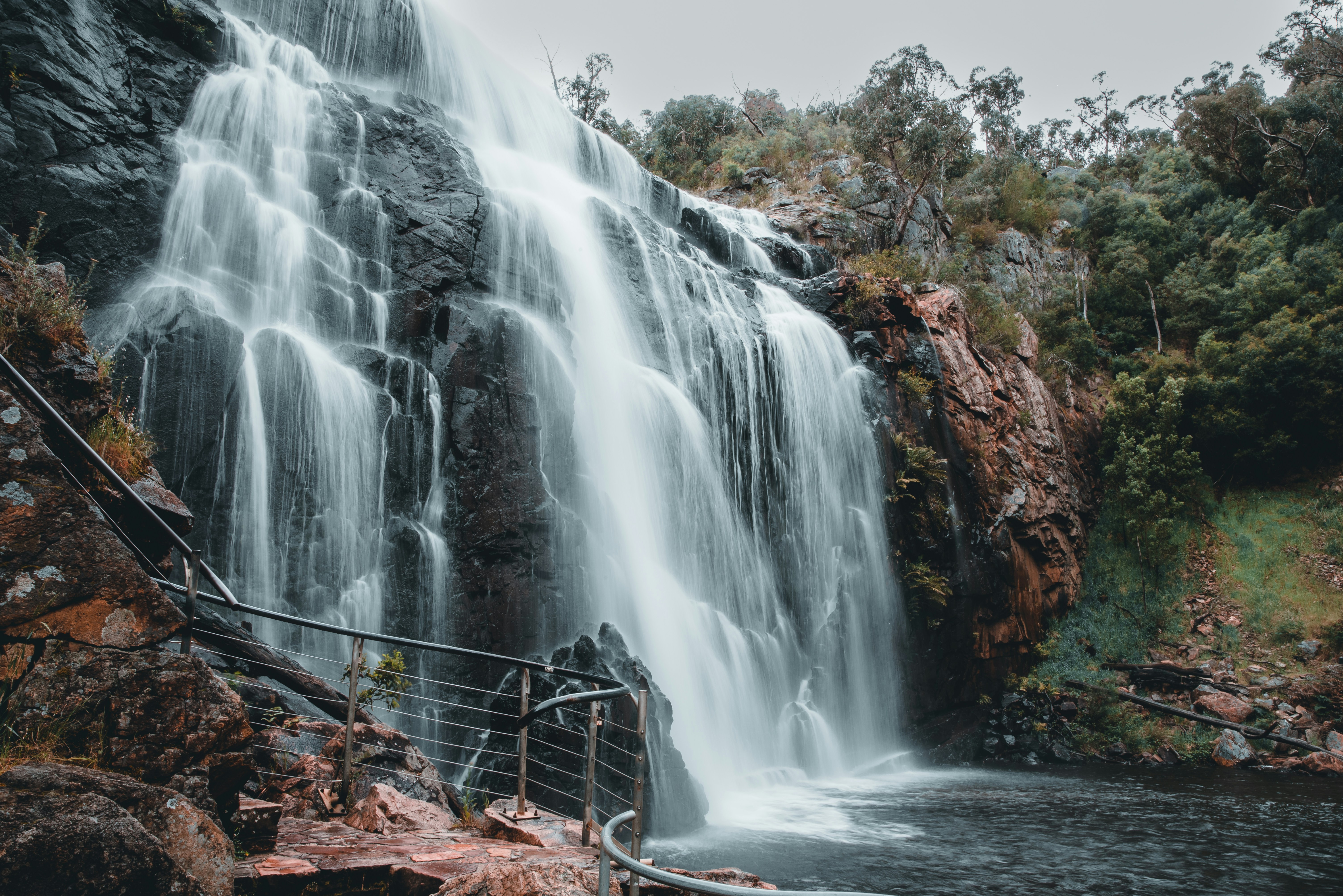 Majestic waterfall flowing down rocky terrain, surrounded by lush greenery and a serene atmosphere.