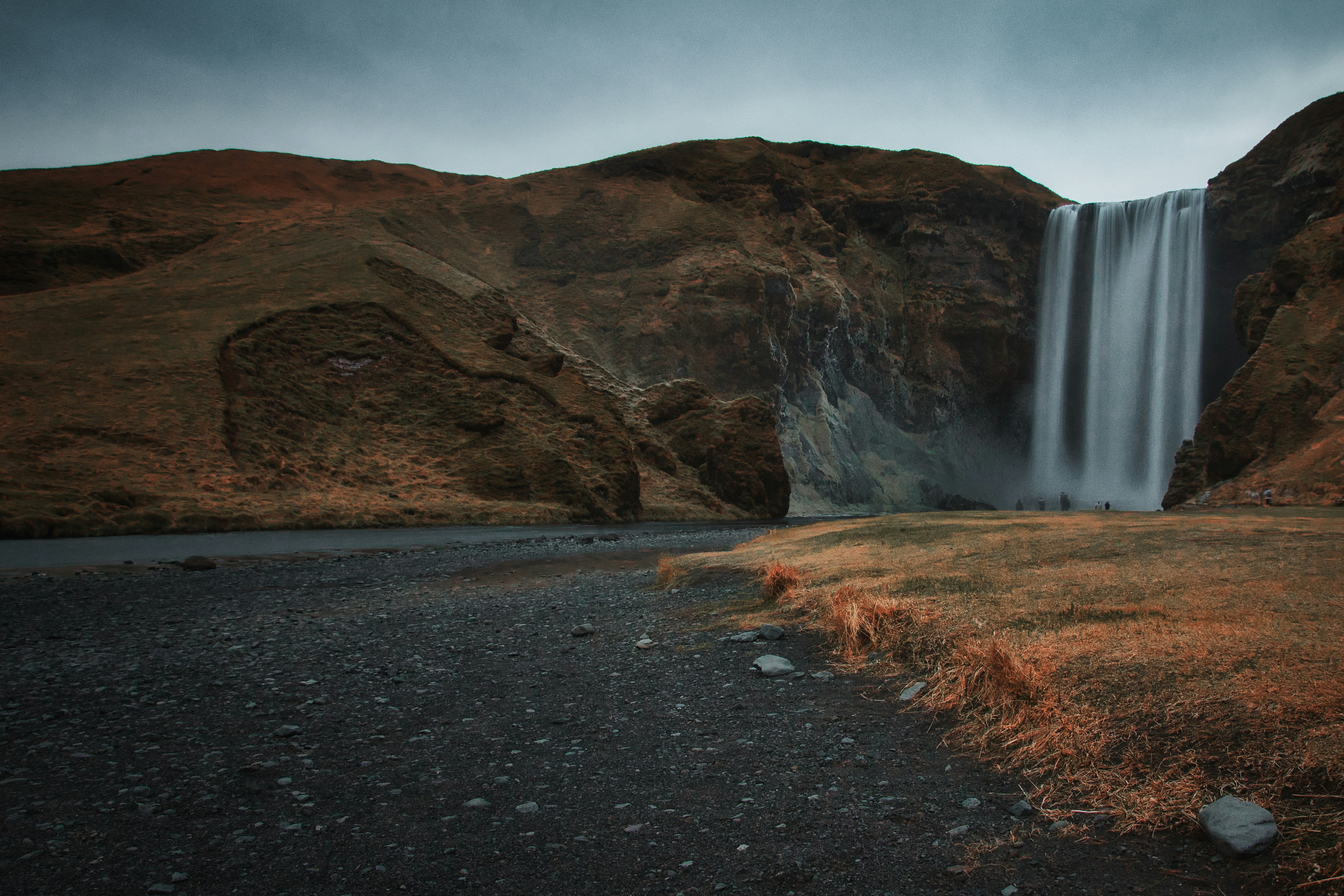 Skogafoss waterfall cascading over rugged cliffs under an overcast sky.