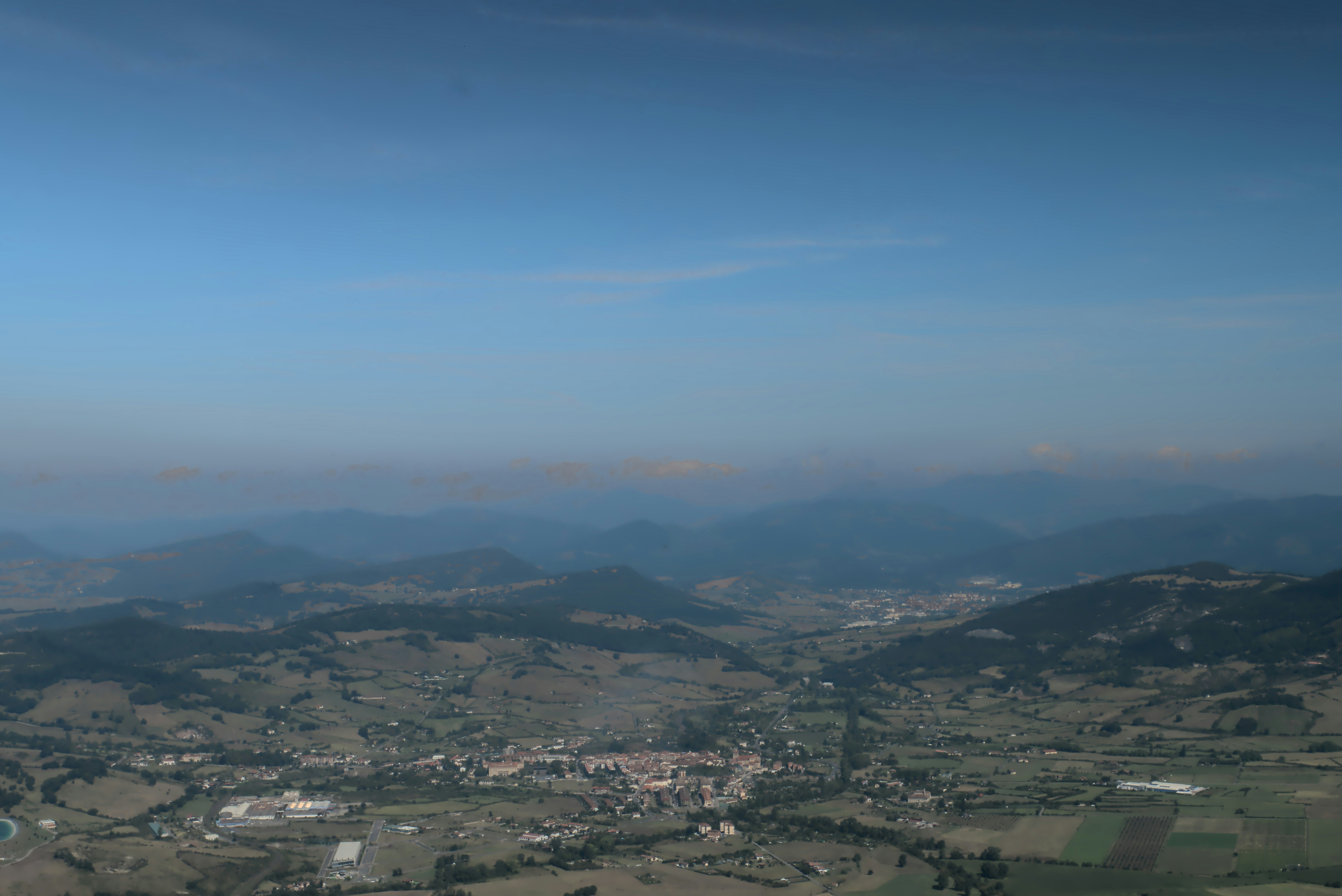 Aerial view showcasing a sprawling valley with a small town nestled among rolling hills and distant mountains under a clear blue sky.