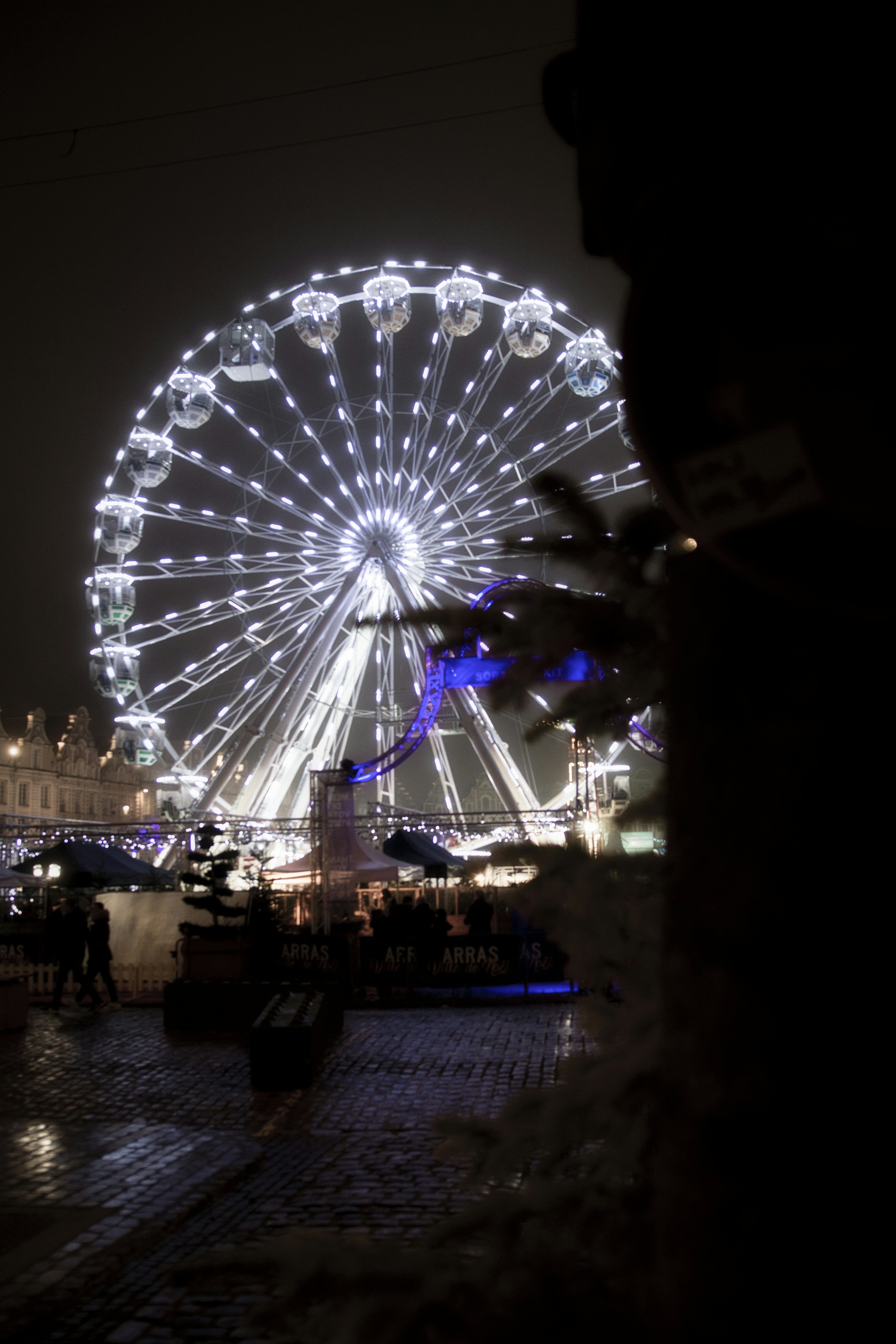 A vibrant Ferris wheel illuminated with dazzling lights, set against a foggy night sky in a festive atmosphere.