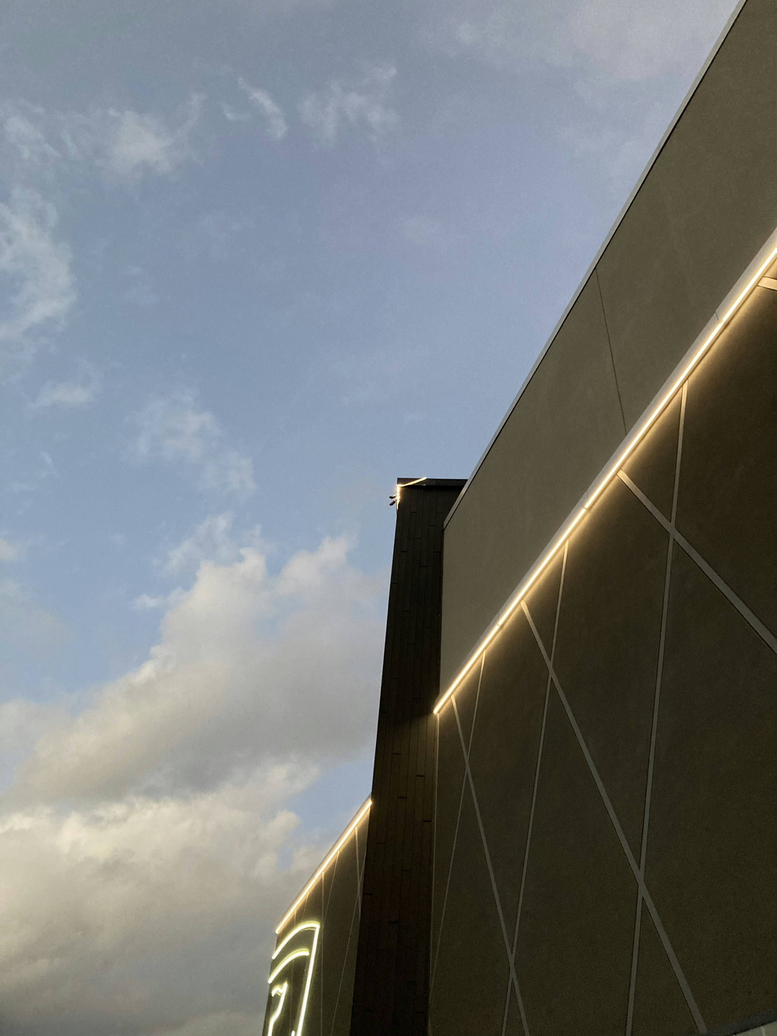 A modern building corner illuminated by soft lighting against a backdrop of a cloudy sky.