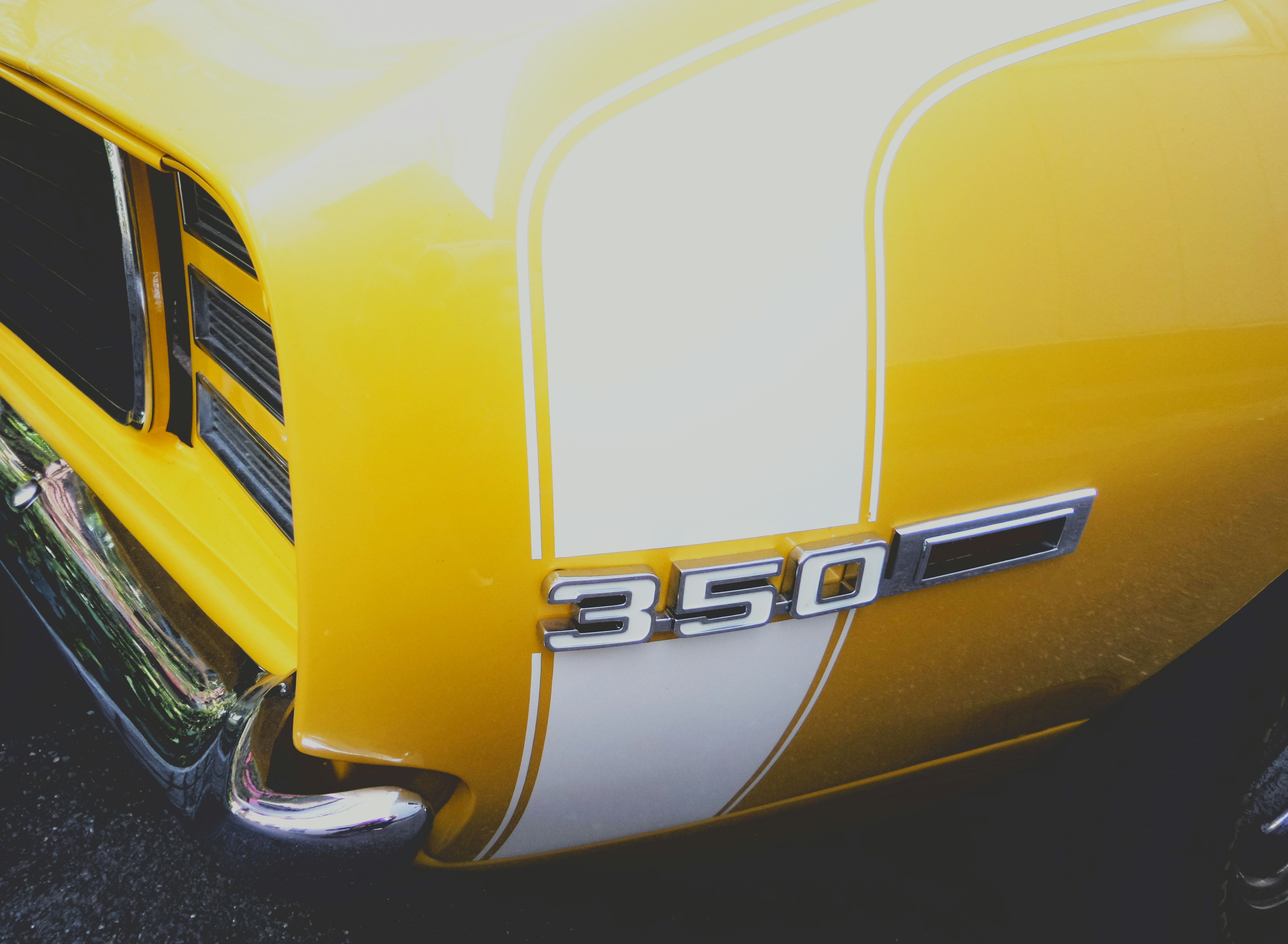 Sunlit Chrome and Racing Stripe: the 350 Badge on a Vintage Yellow Muscle Car