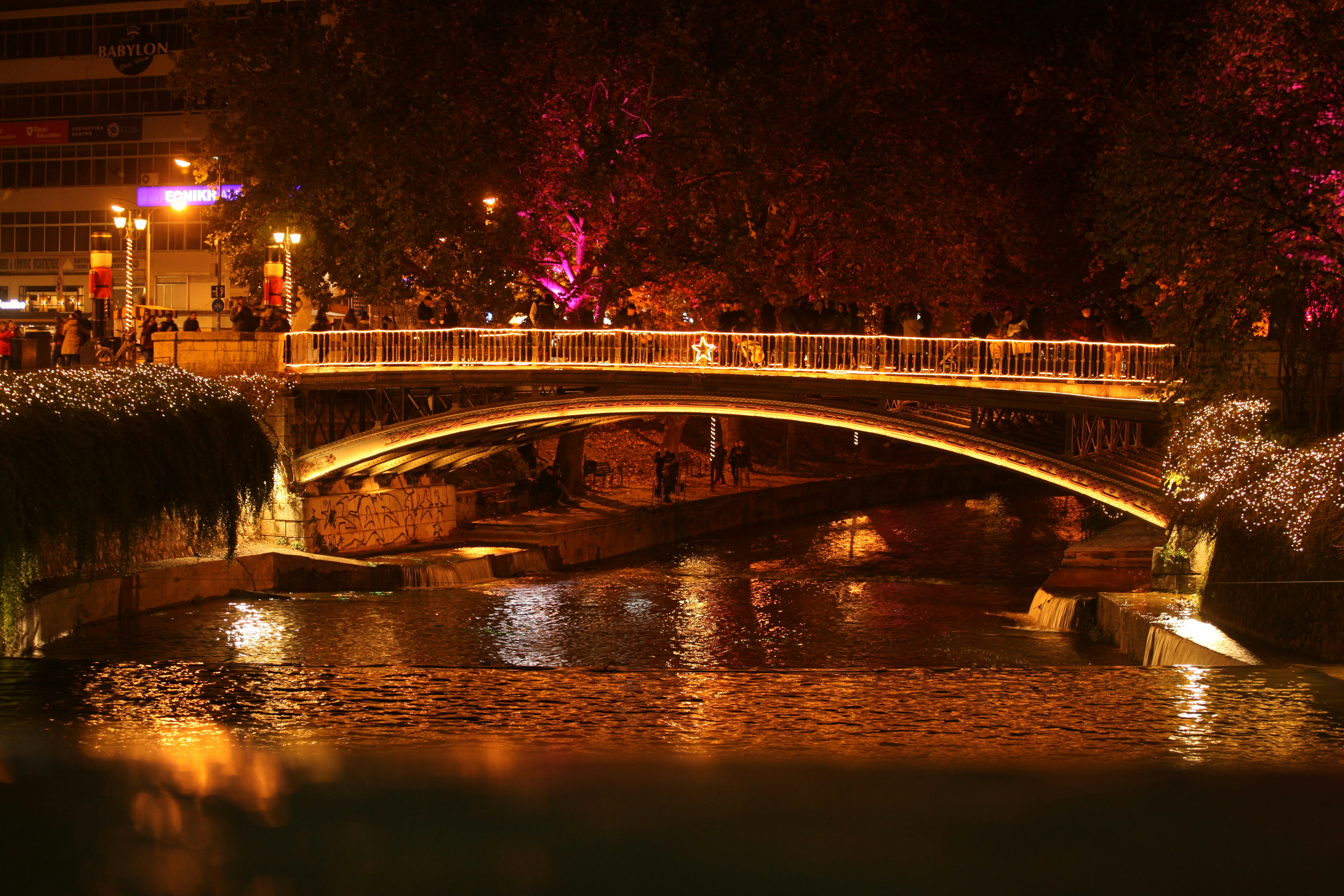 Arched bridge glowing with warm lights over a calm river at night.