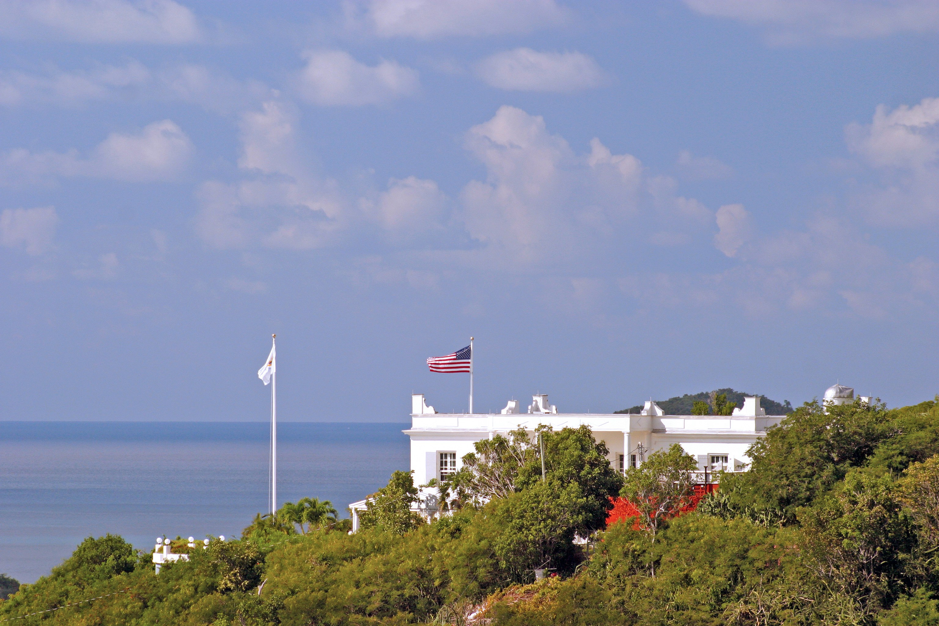 Historic building overlooking the ocean, framed by lush greenery and a waving American flag. The scene conveys a sense of tranquility and connection to nature.