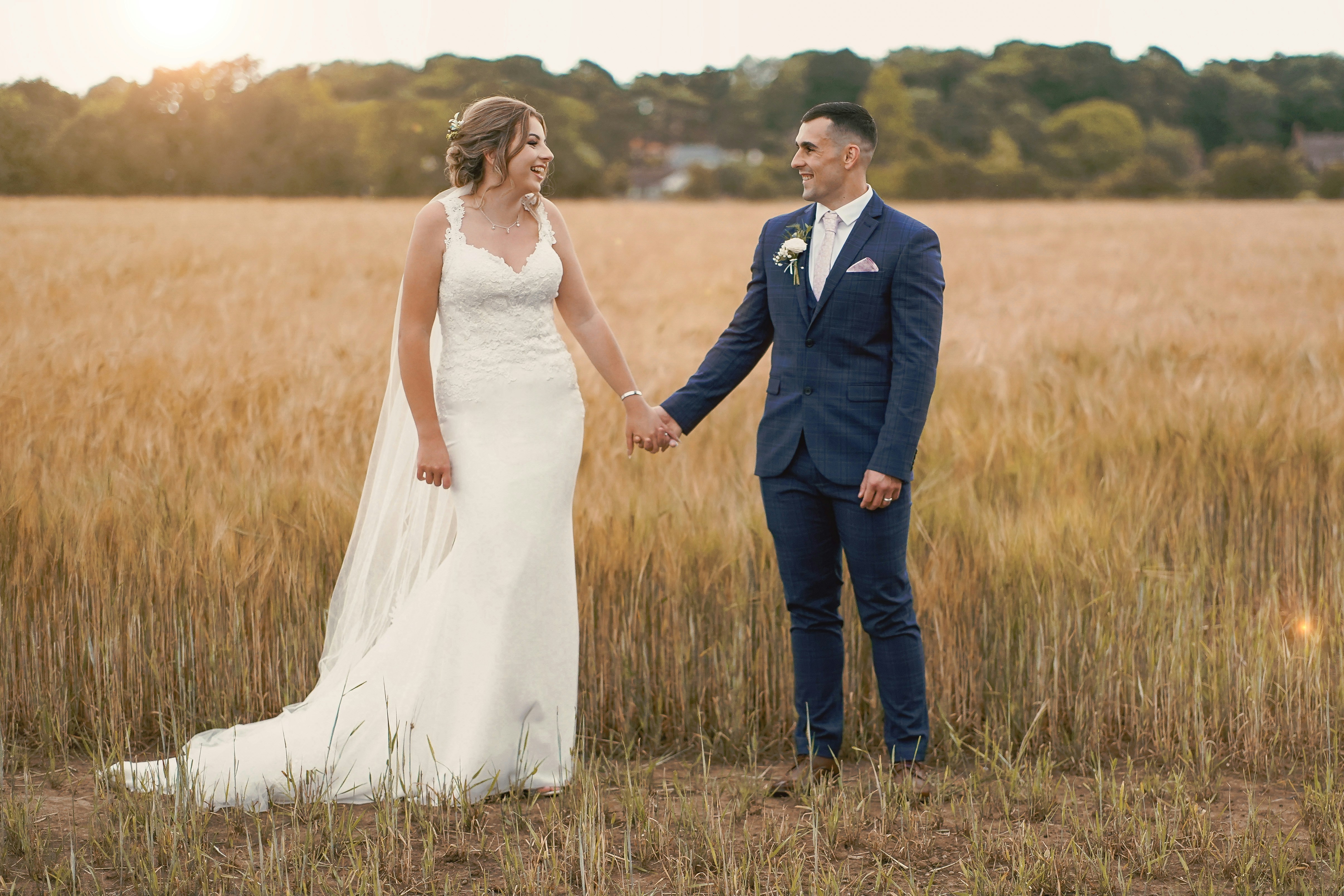 Bride and groom holding hands in a sunlit field of tall grass.