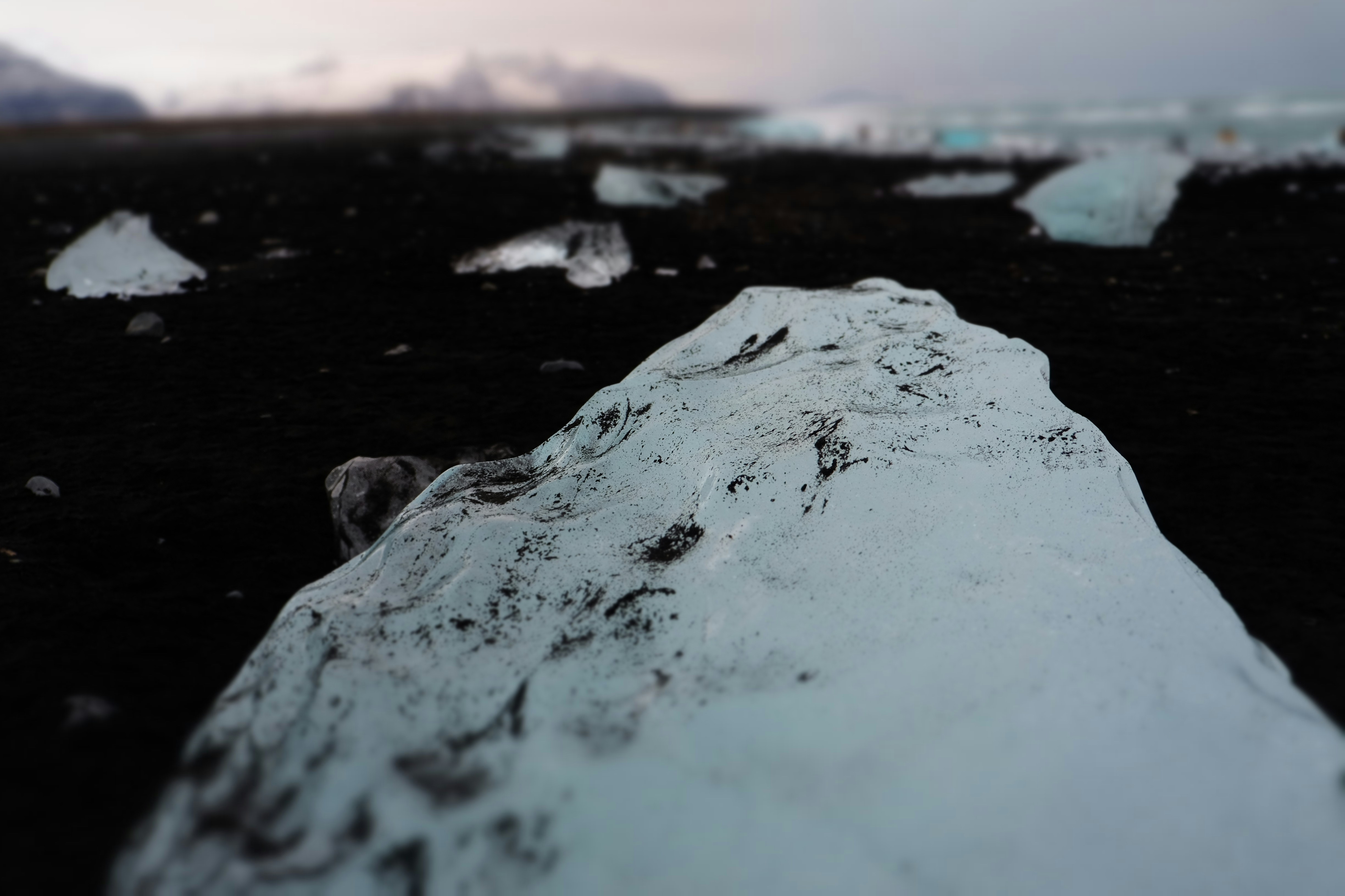 Chunk of glacial ice resting on a black volcanic beach, surrounded by scattered ice fragments under a moody sky.