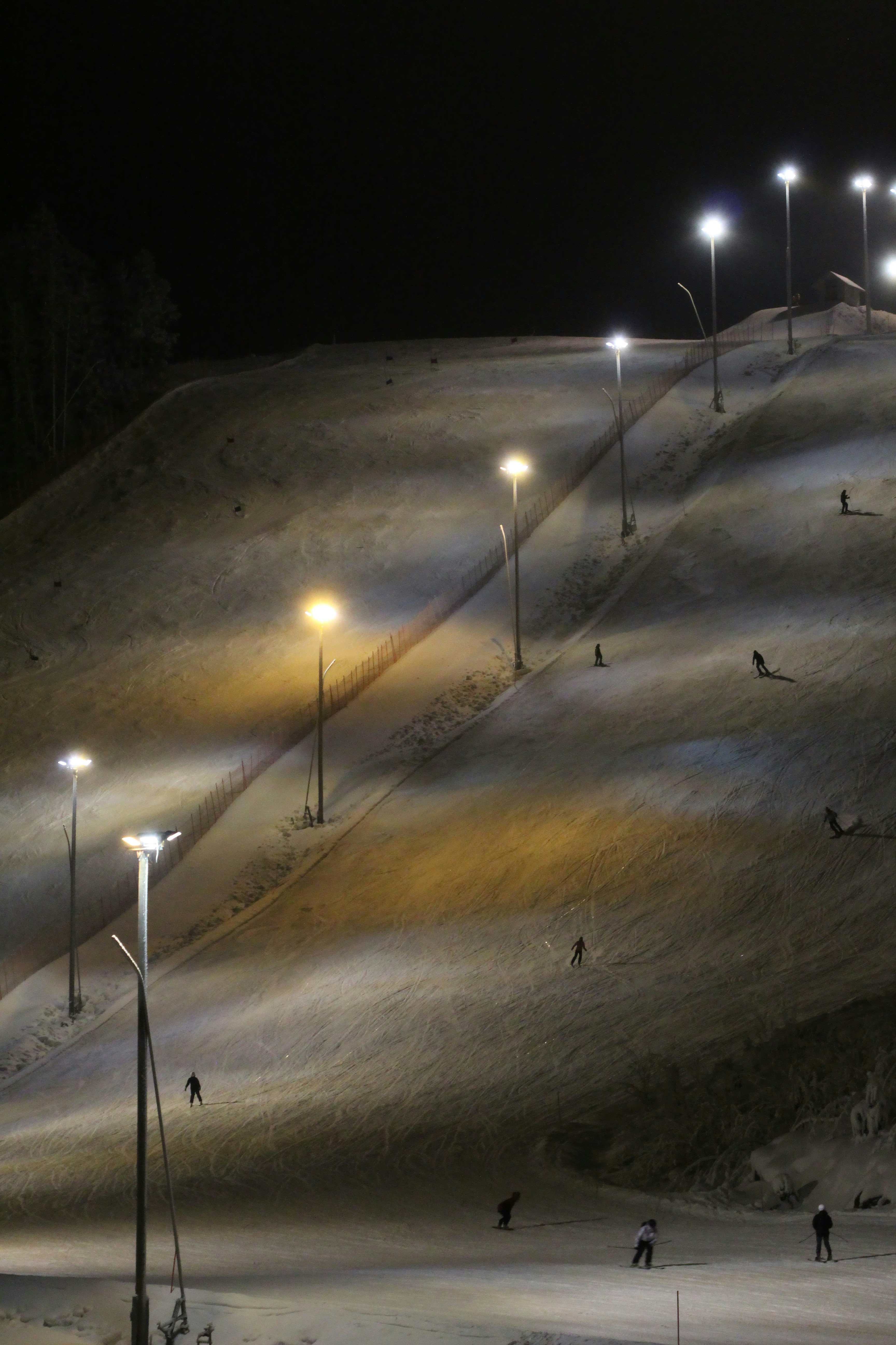 Skiers navigate illuminated slopes under a night sky, showcasing the thrill of winter sports. Bright lights highlight the snowy terrain.
