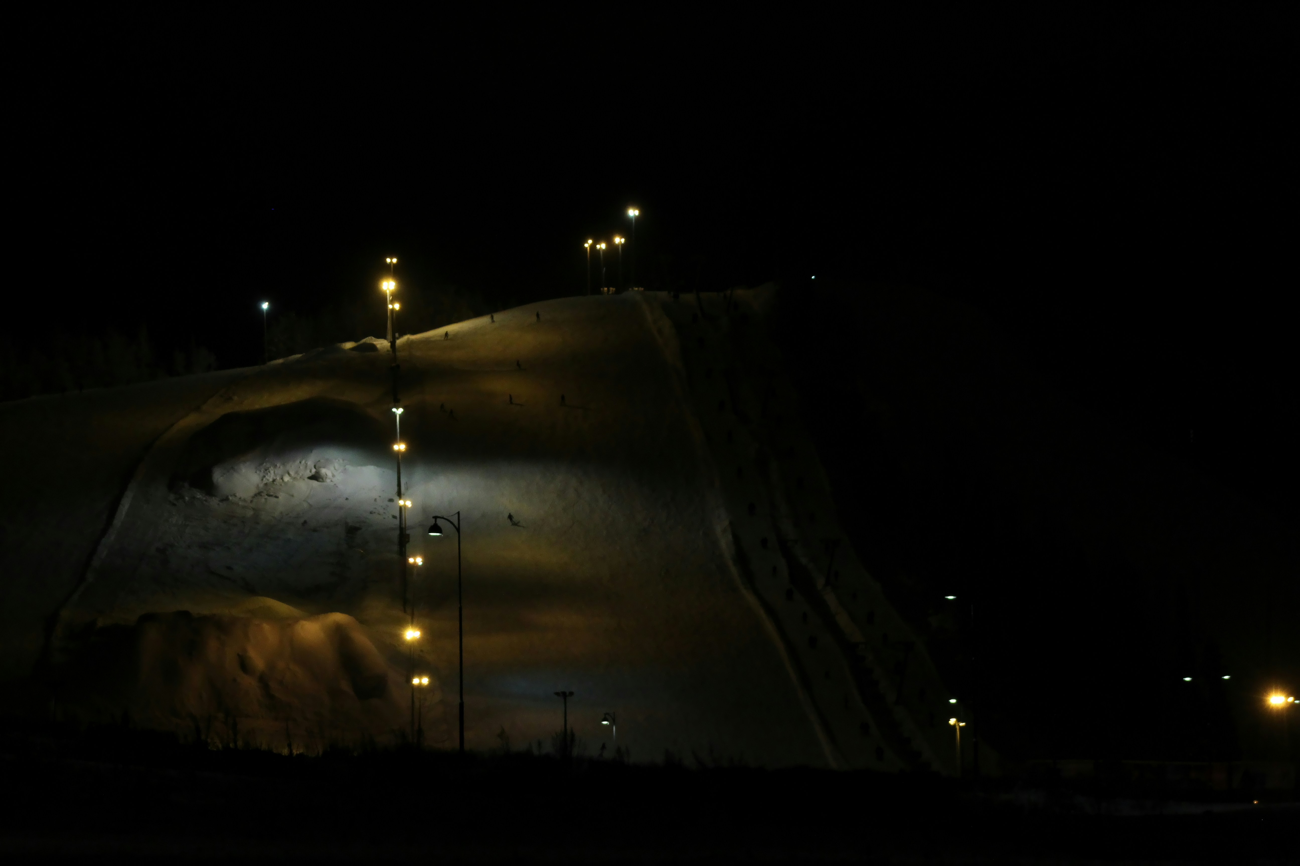 Ski slope illuminated by bright lights under a dark sky, showcasing a winter sports scene at night.