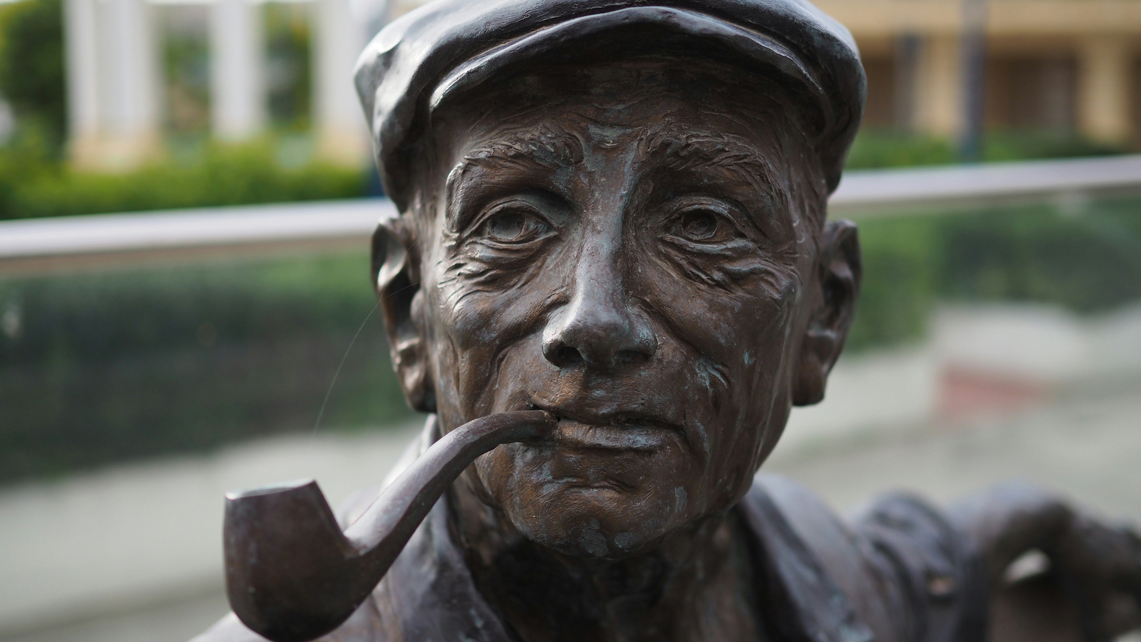Close-up of a bronze sculpture depicting an elderly man with a pipe, showcasing intricate details and textures. The artwork captures a moment of contemplation.