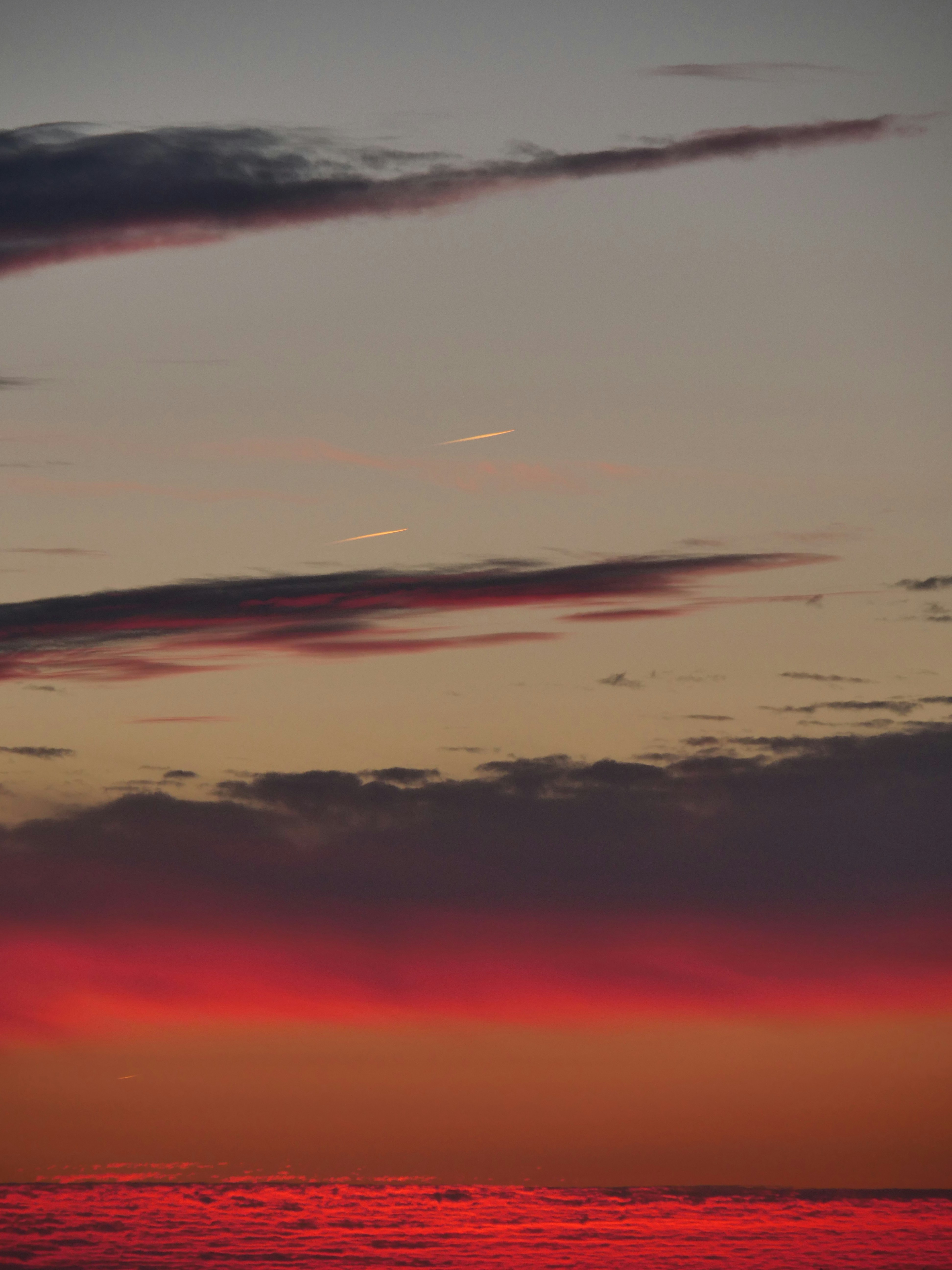 Crimson Crest on a Calm Sea: Sunset with Subtle Contrails