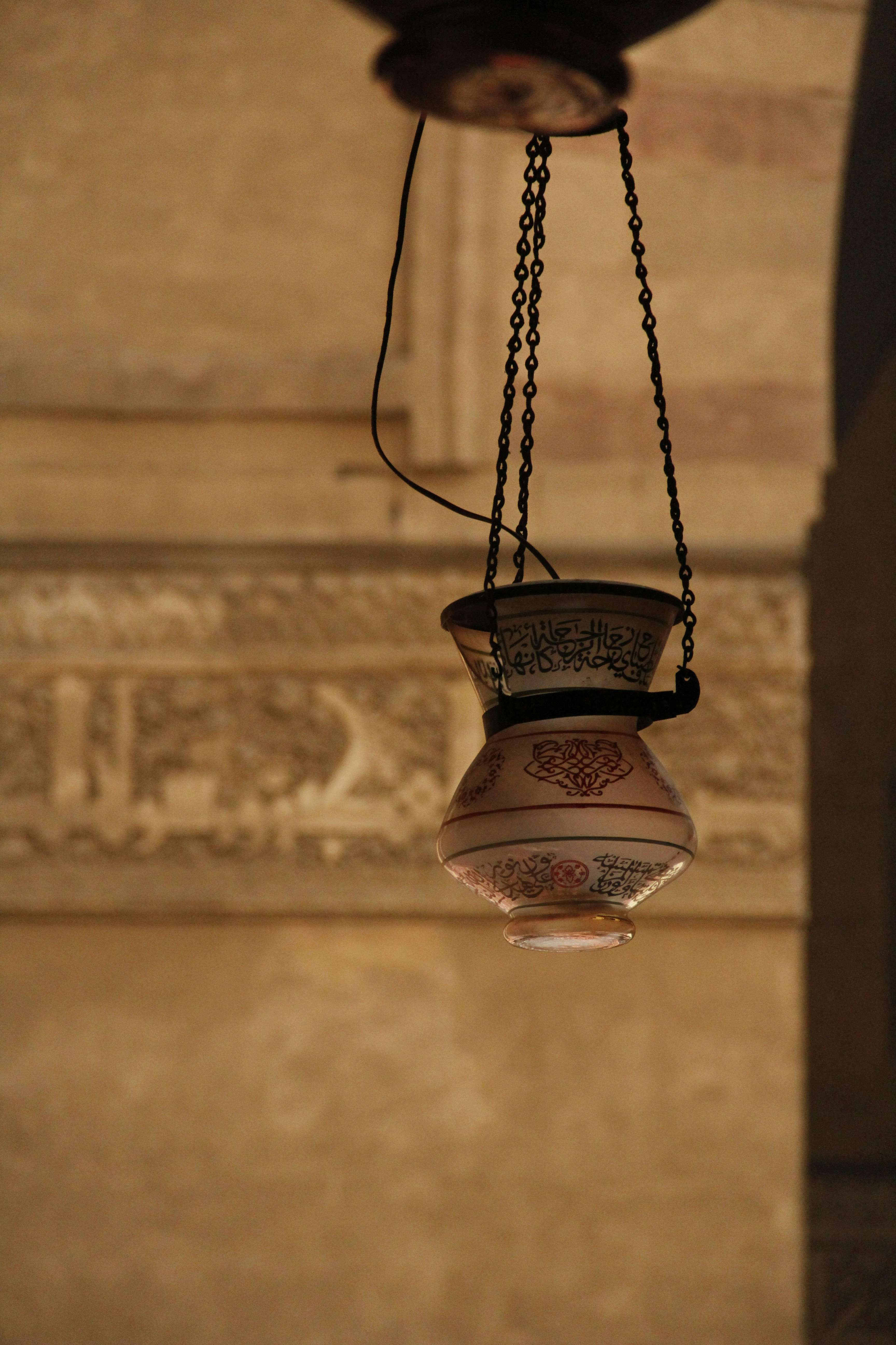 A beautifully crafted hanging lantern adorned with intricate designs, suspended against a softly lit stone background, showcasing historical artistry.