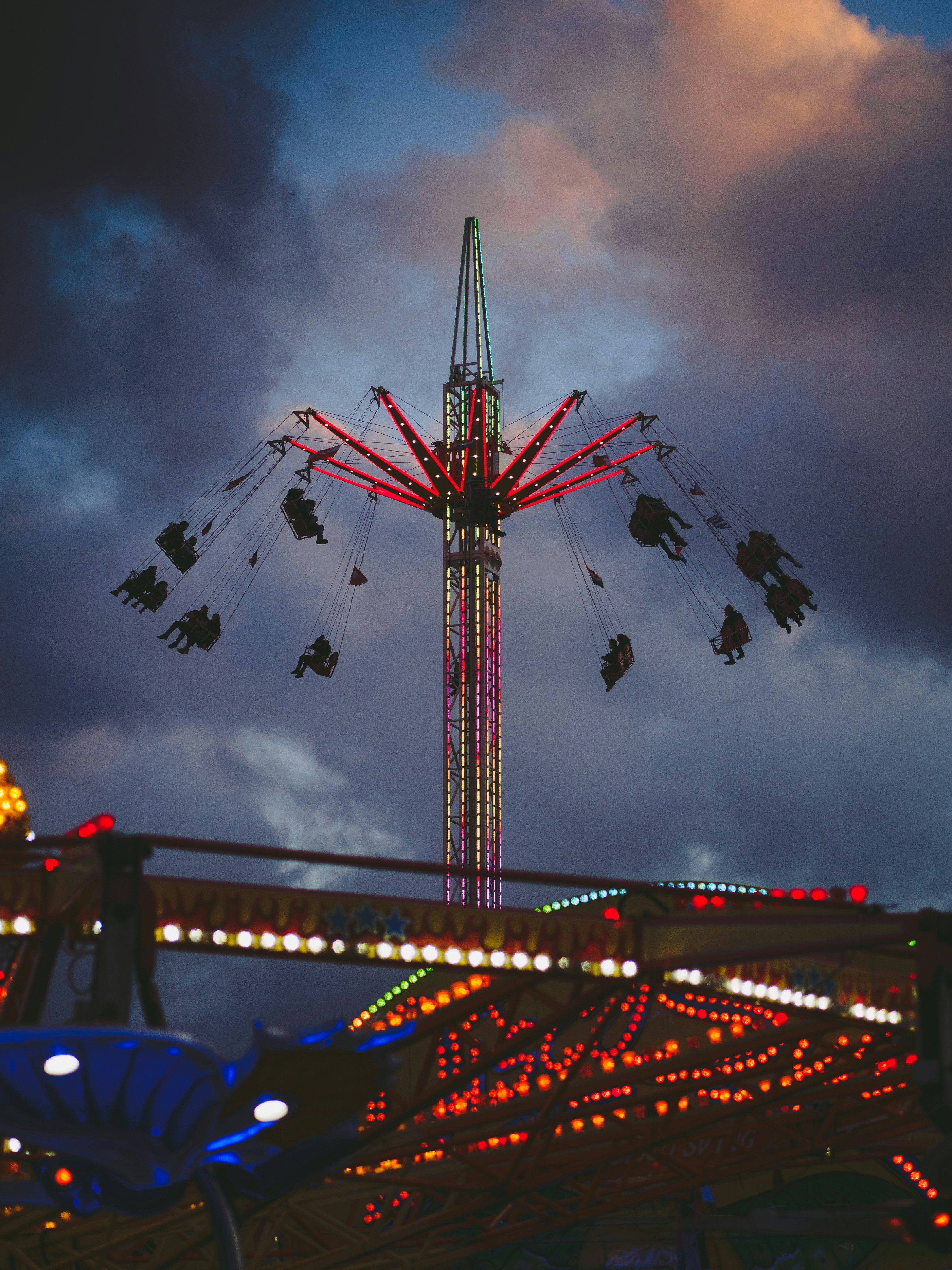 Colorful swing ride illuminated against a dramatic evening sky, capturing the thrill of amusement park fun.