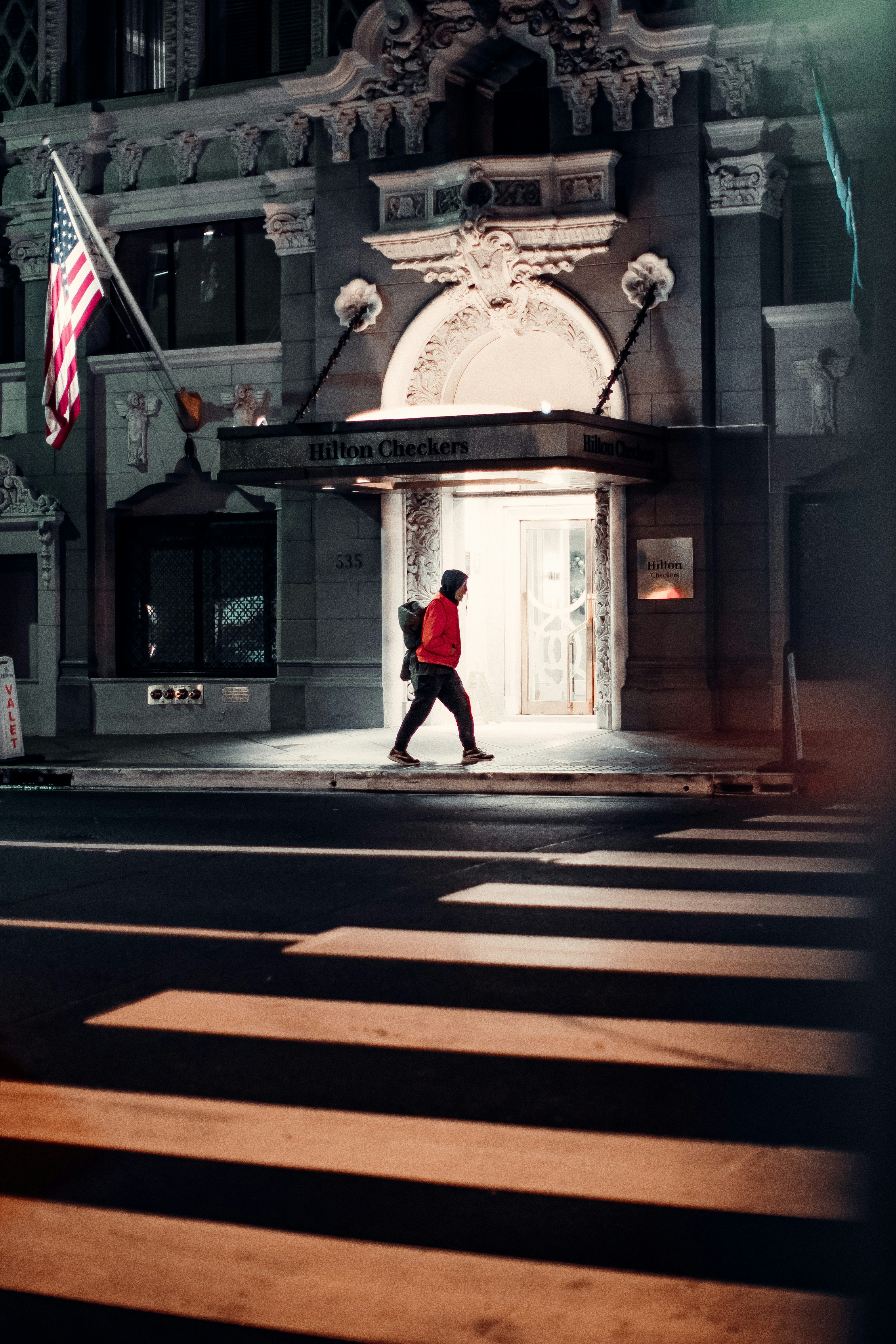 Red-hooded figure steps into a softly lit façade of a vintage city theater