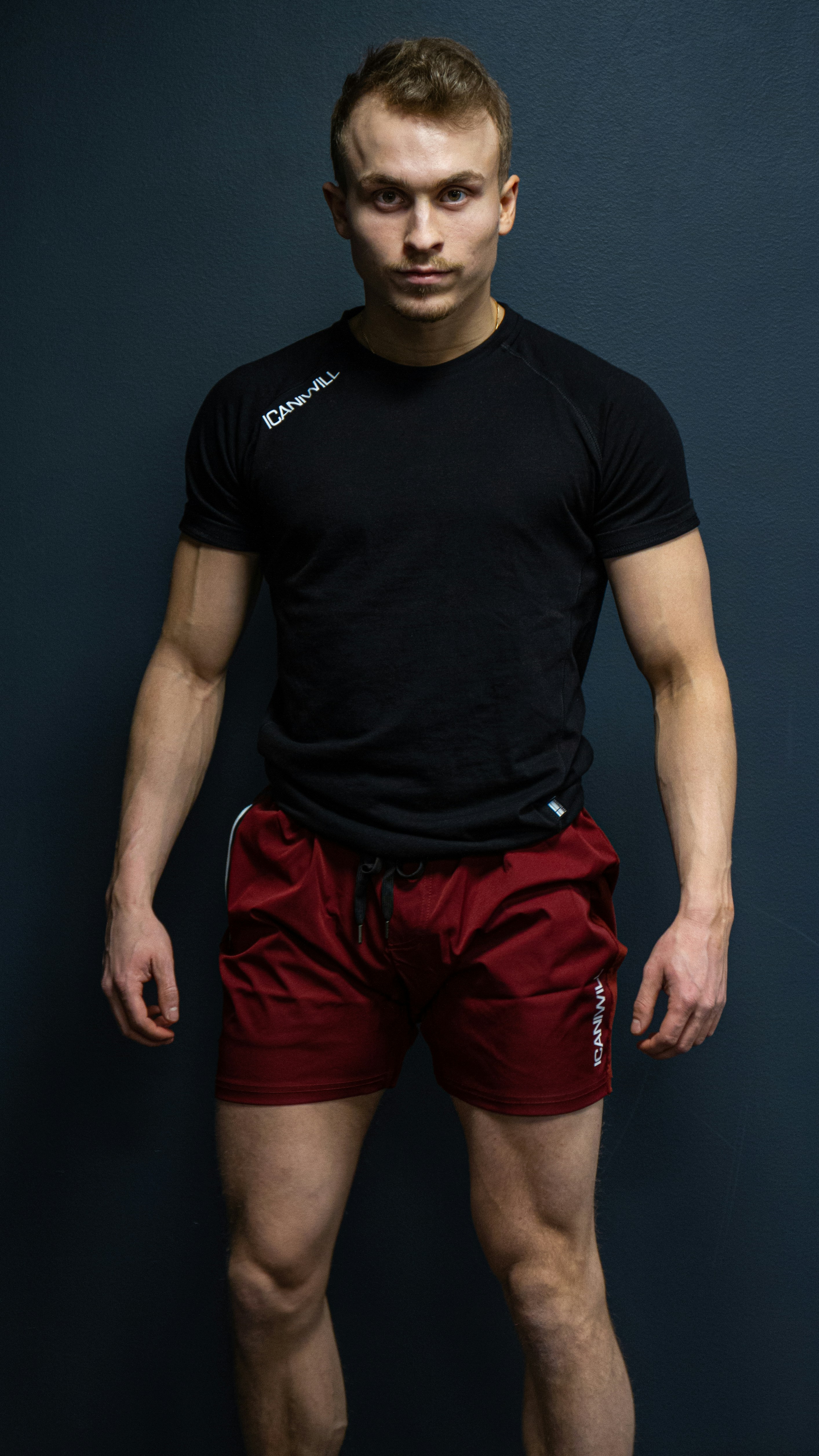 Athlete posing confidently against a dark background, showcasing athletic wear and muscular build.