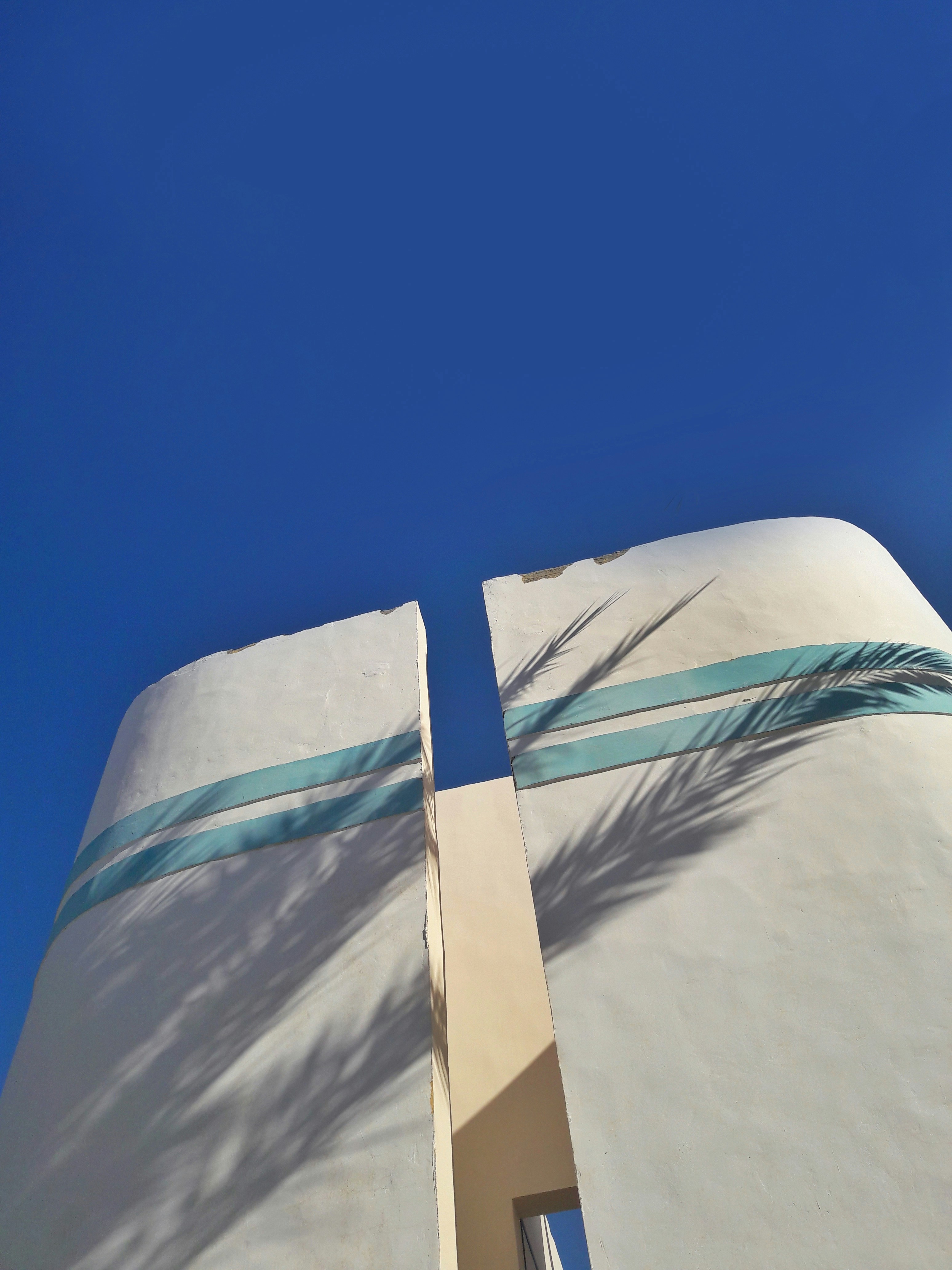Two curved walls with a blue stripe stand against a vibrant blue sky, casting shadows on the surface below.