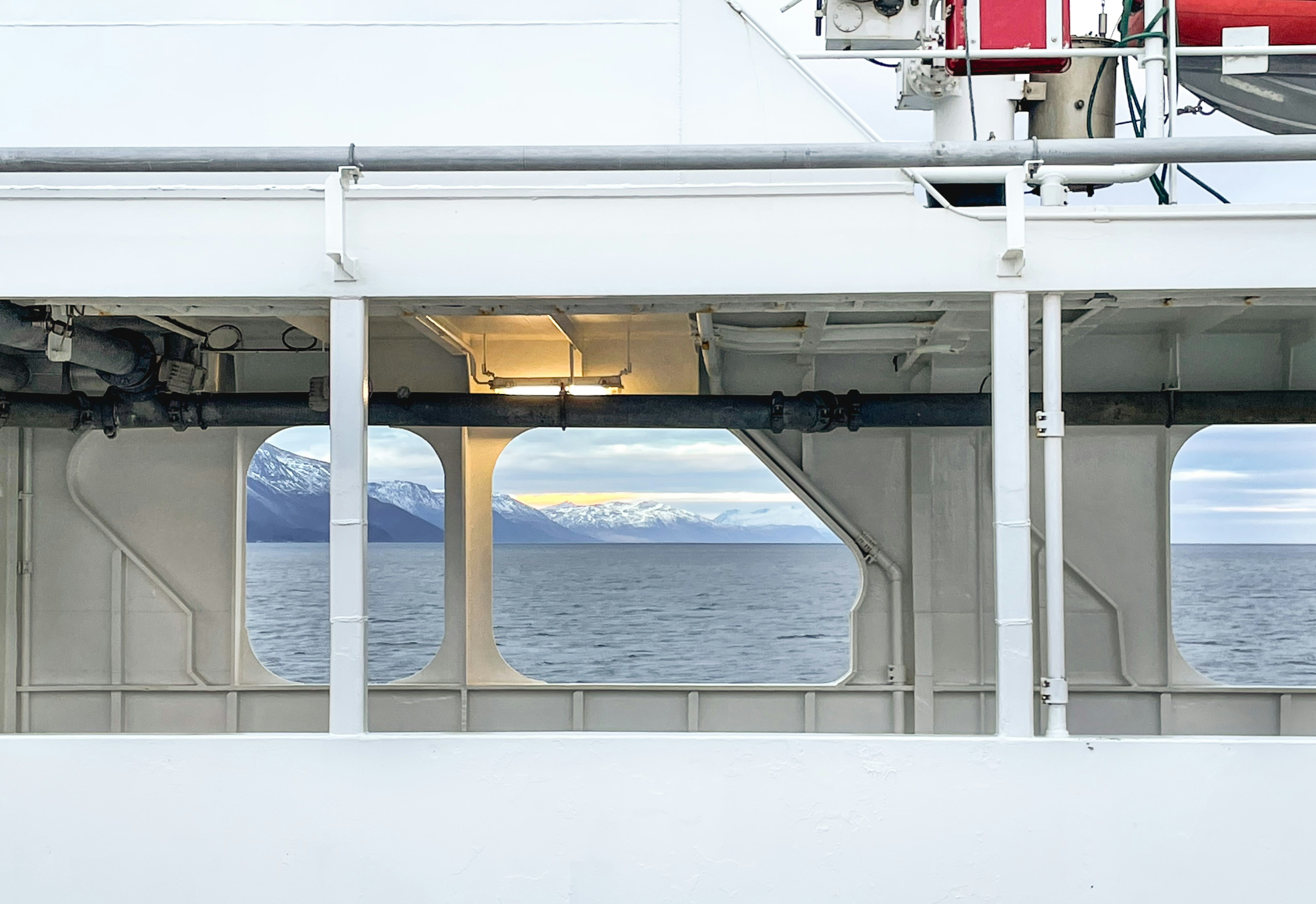 View through a ship's window showcasing a tranquil seascape with distant mountains under a soft sky.